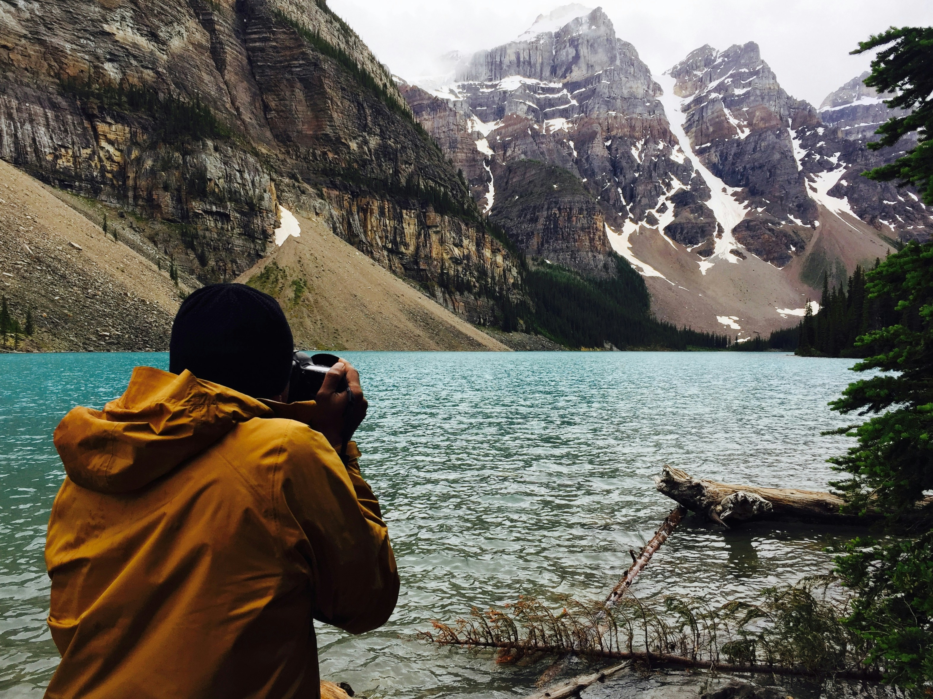 Orange-Raincoat Photographer Capturing Turquoise Alpine Lake