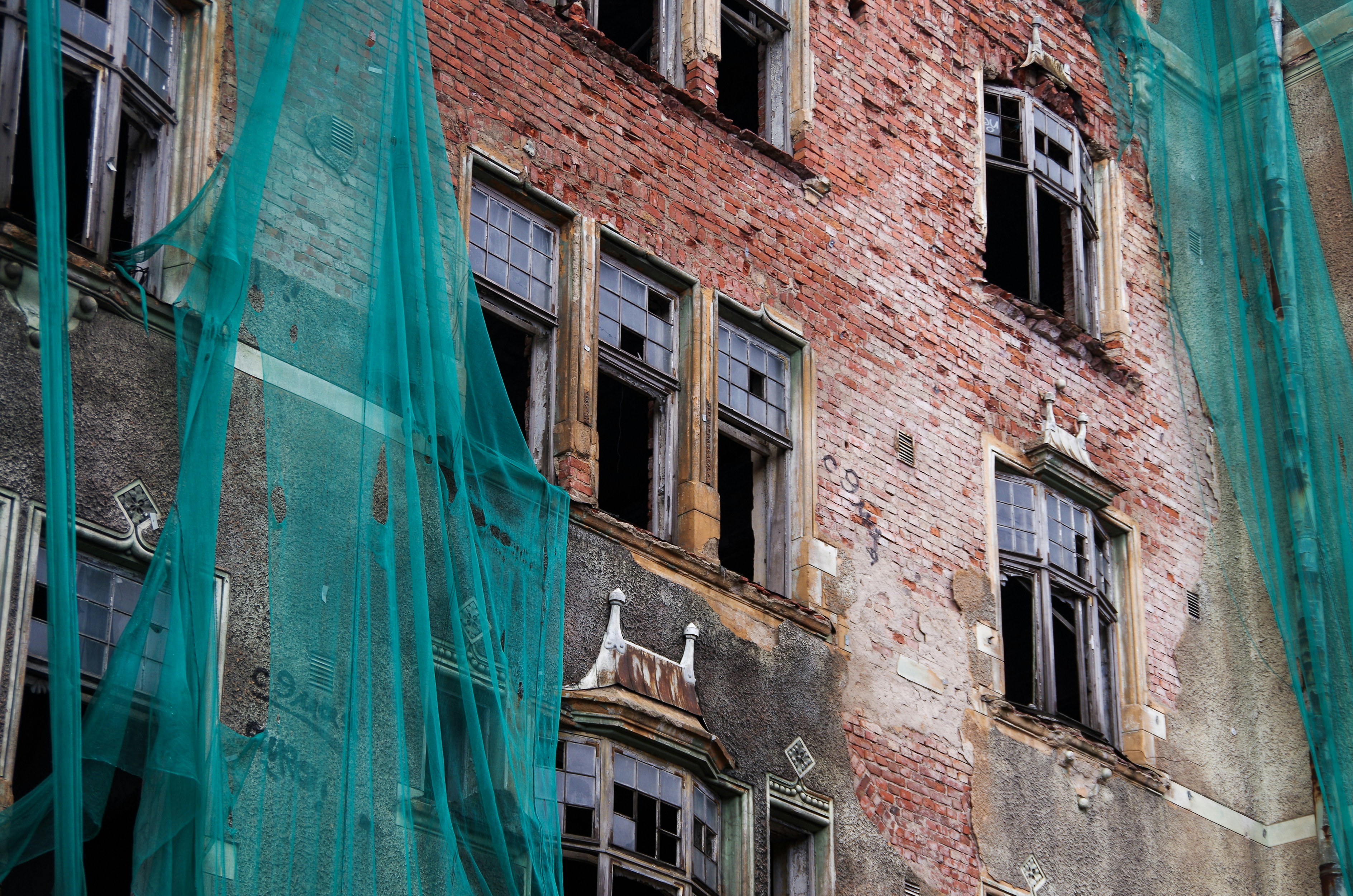 Weathered brick walls adorned with flowing teal fabric, revealing broken windows and a sense of forgotten history.