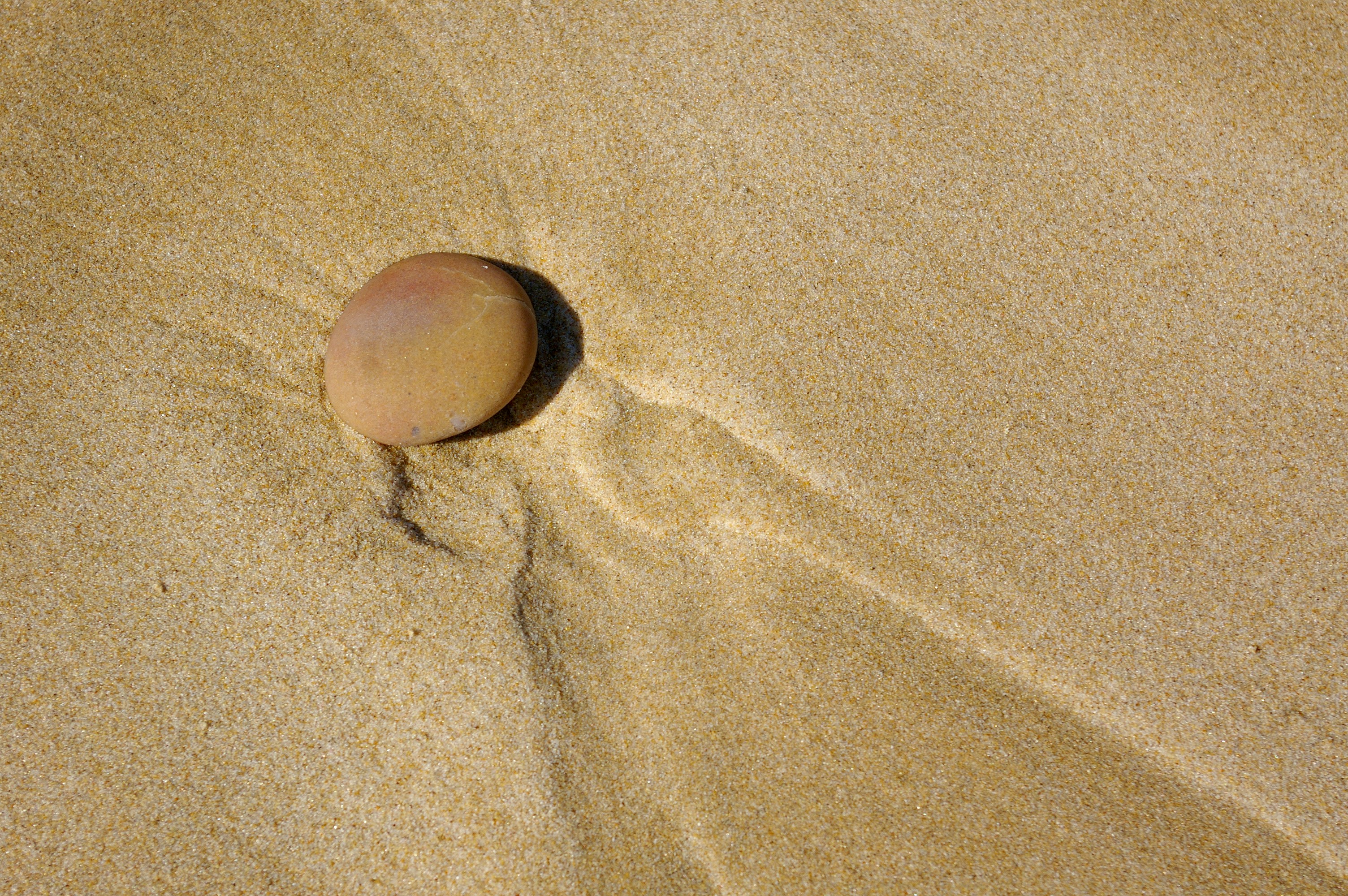 Smooth, rounded stone resting on a textured sandy surface, with subtle patterns carved by the wind. 