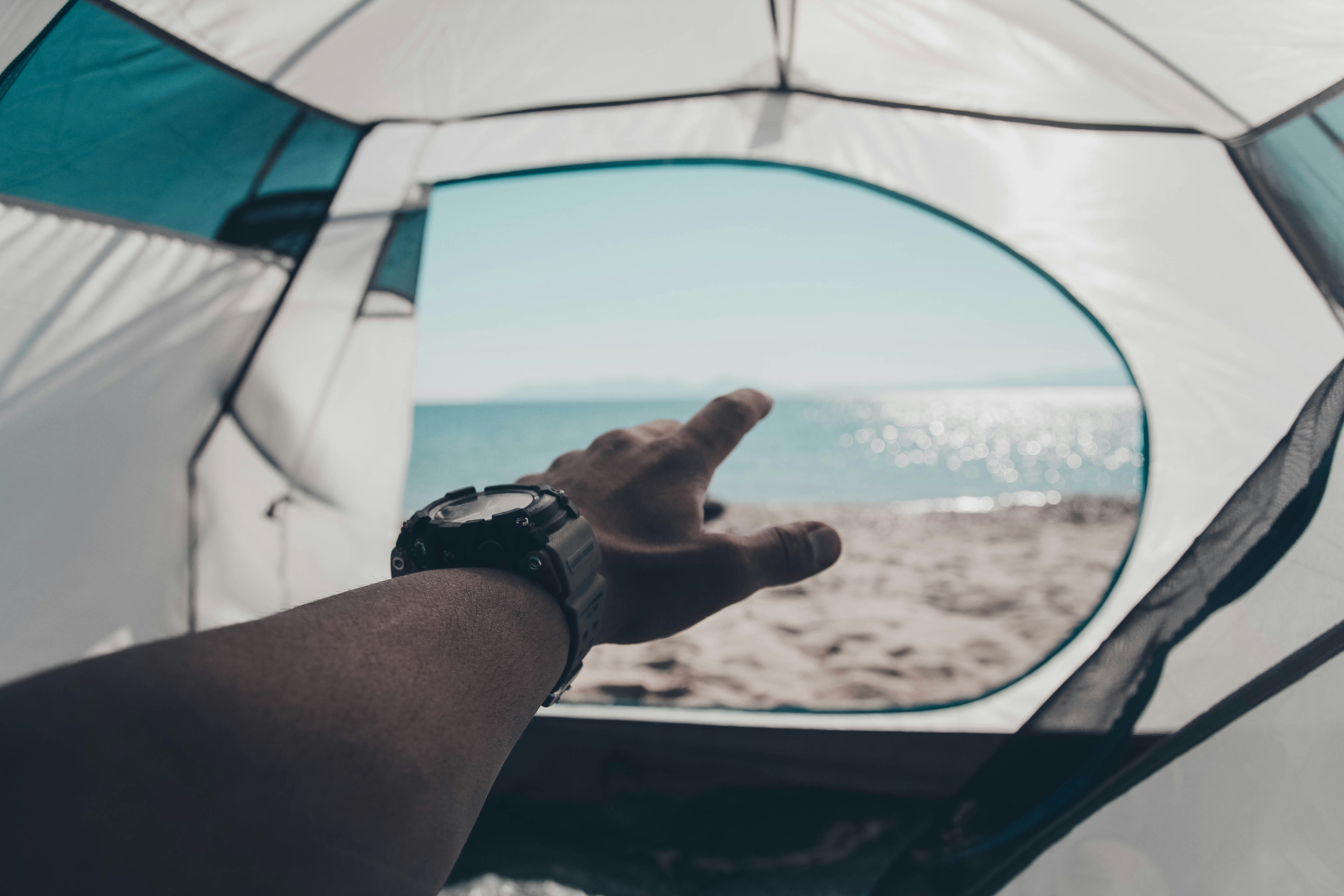 Through the Tent Opening: A Hand Reaches Toward a Sunlit Beach