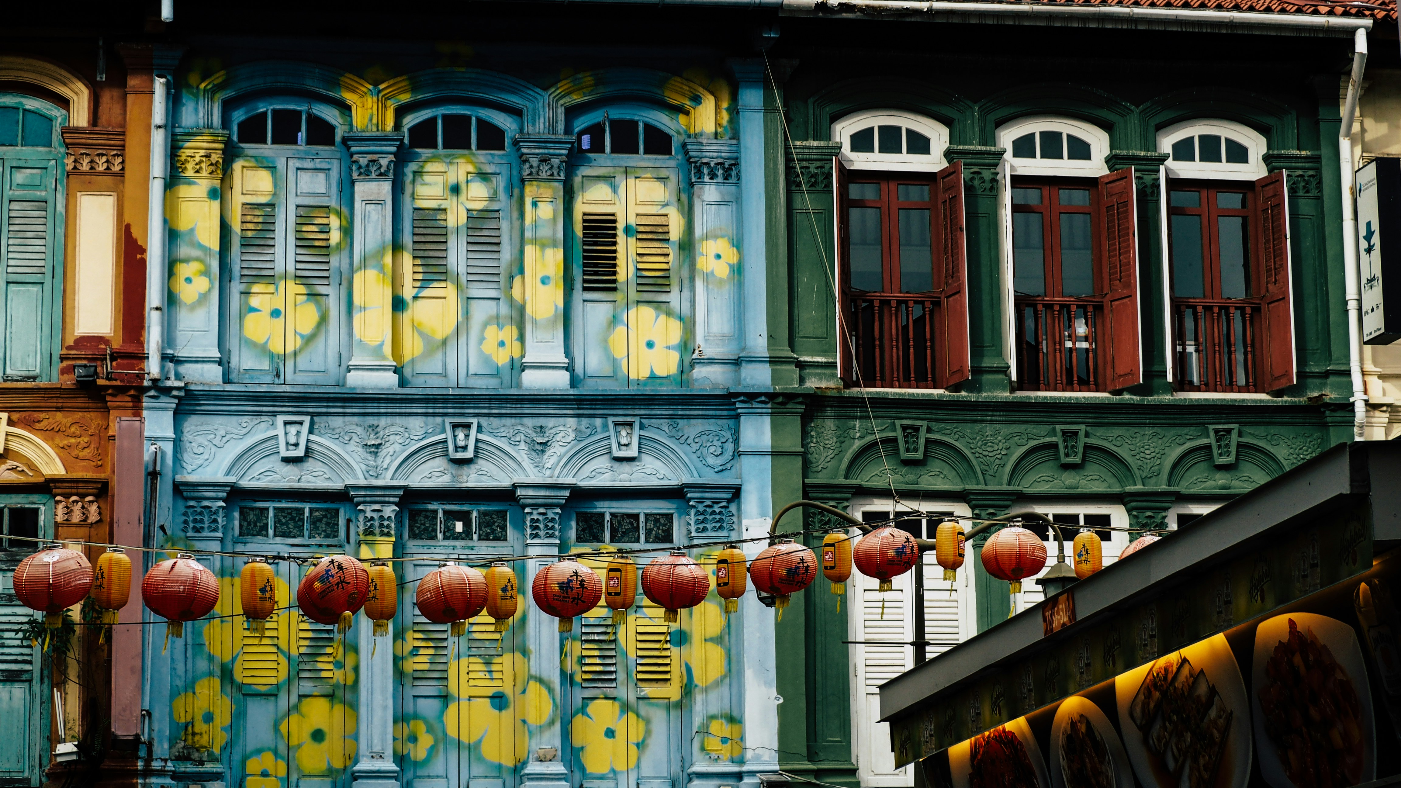 Charming heritage buildings adorned with floral murals and traditional lanterns create a lively street scene. The contrasting colors highlight the cultural richness of the area.