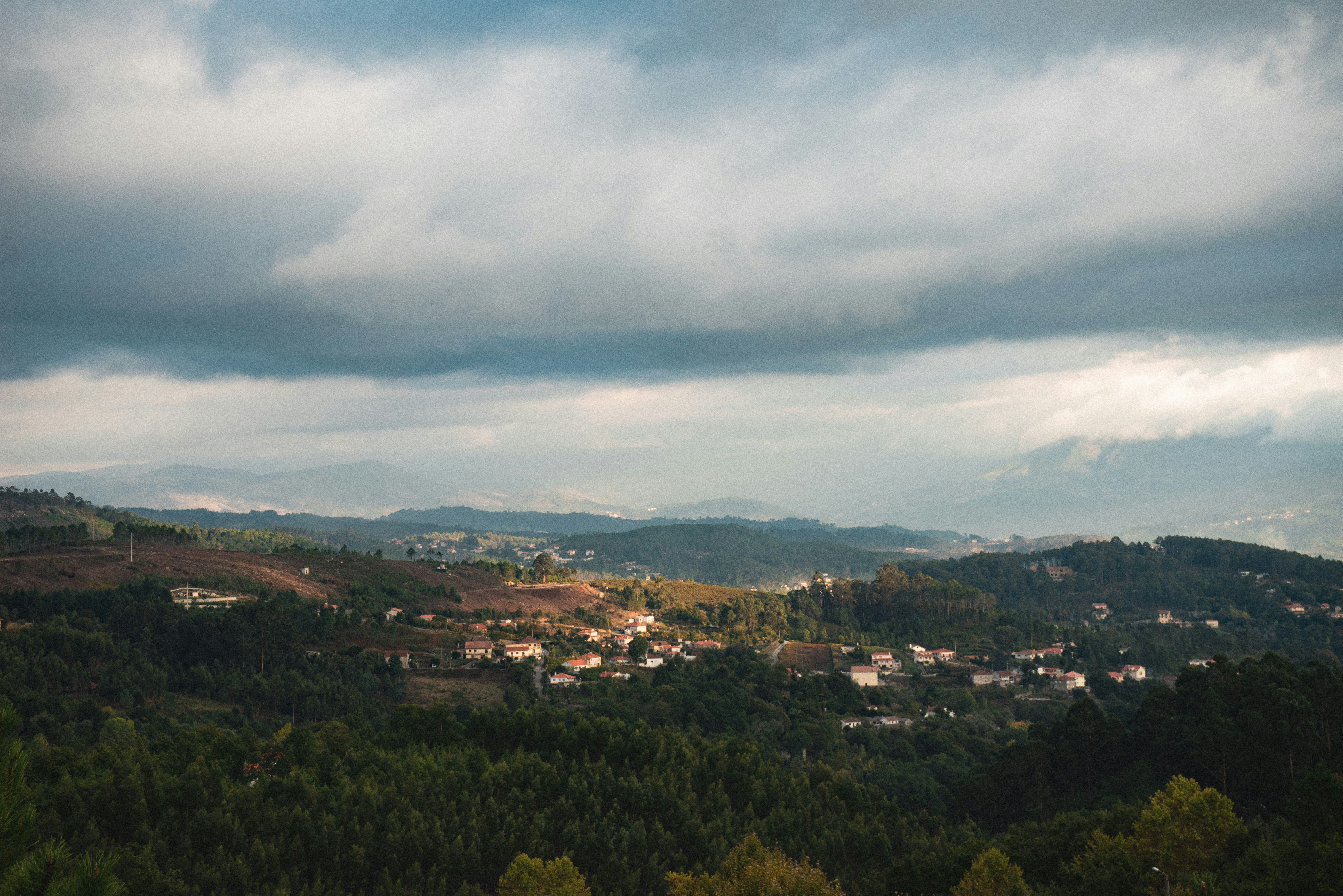 Clouds part to reveal sunlight illuminating a village nestled in verdant hills.