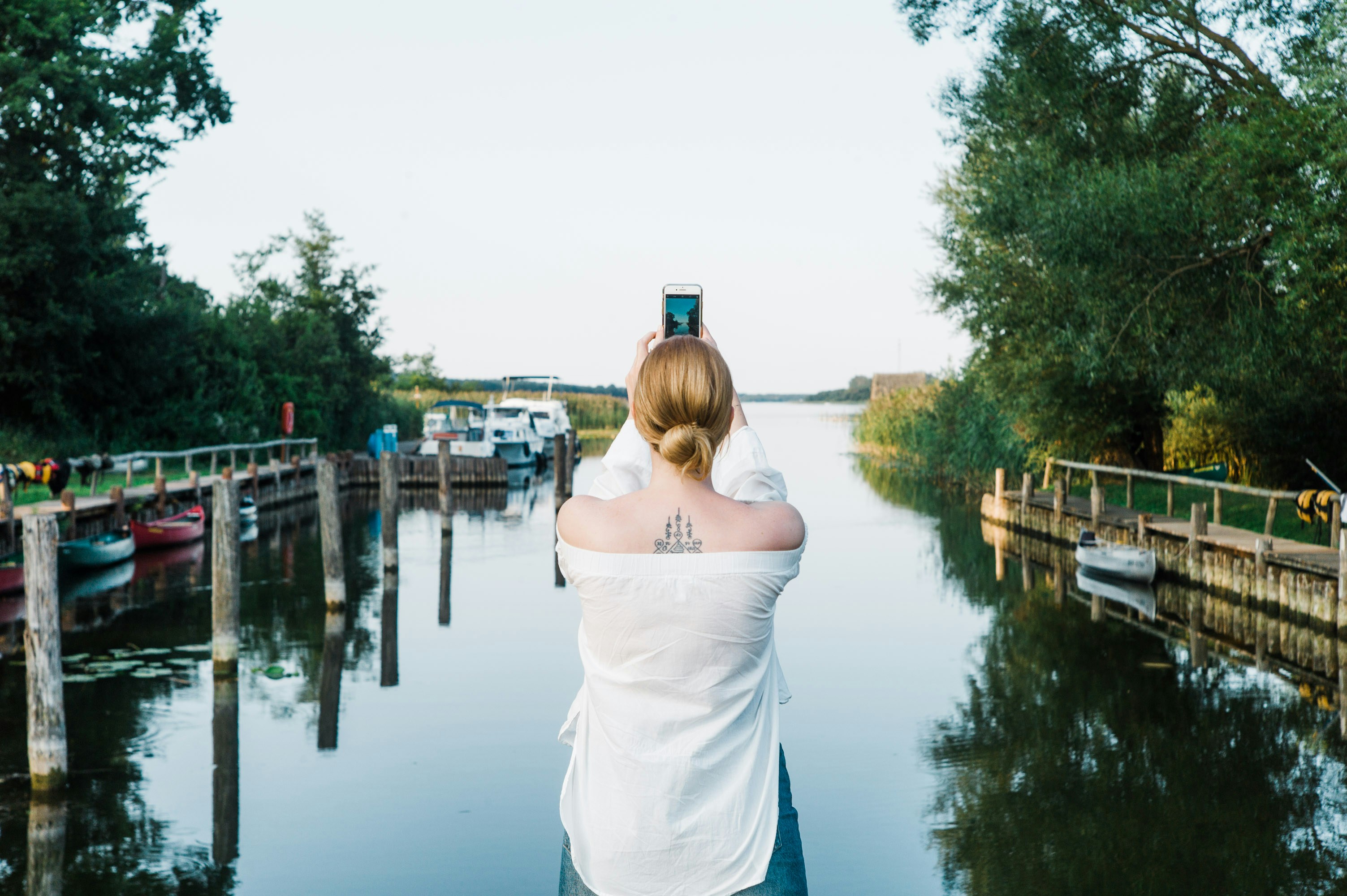 Person capturing a scenic view of a calm waterway lined with boats and greenery, showcasing a moment of connection with nature.