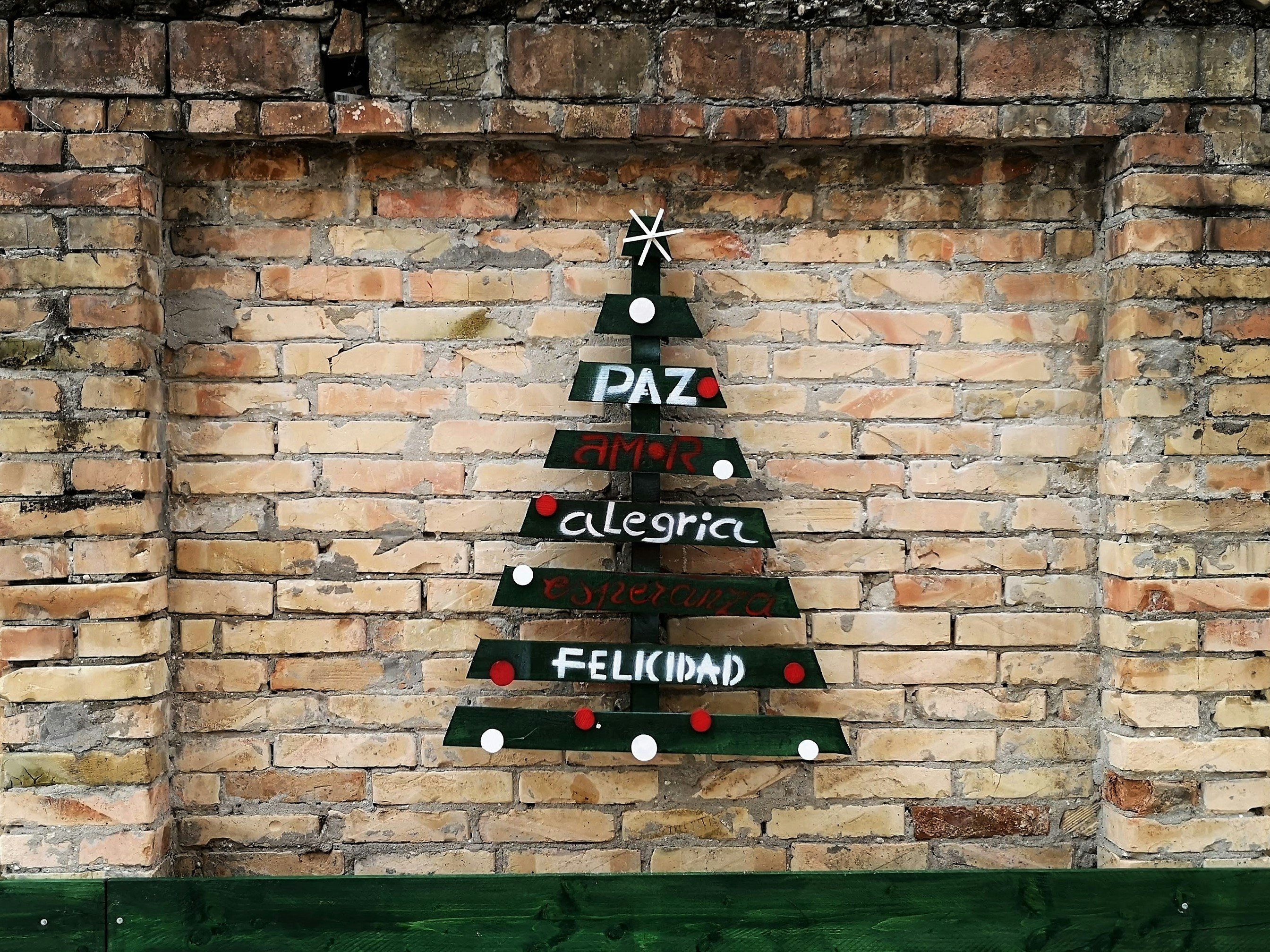 Decorative Christmas tree with words 'Paz,' 'Alegría,' and 'Felicidad' mounted on a brick wall.
