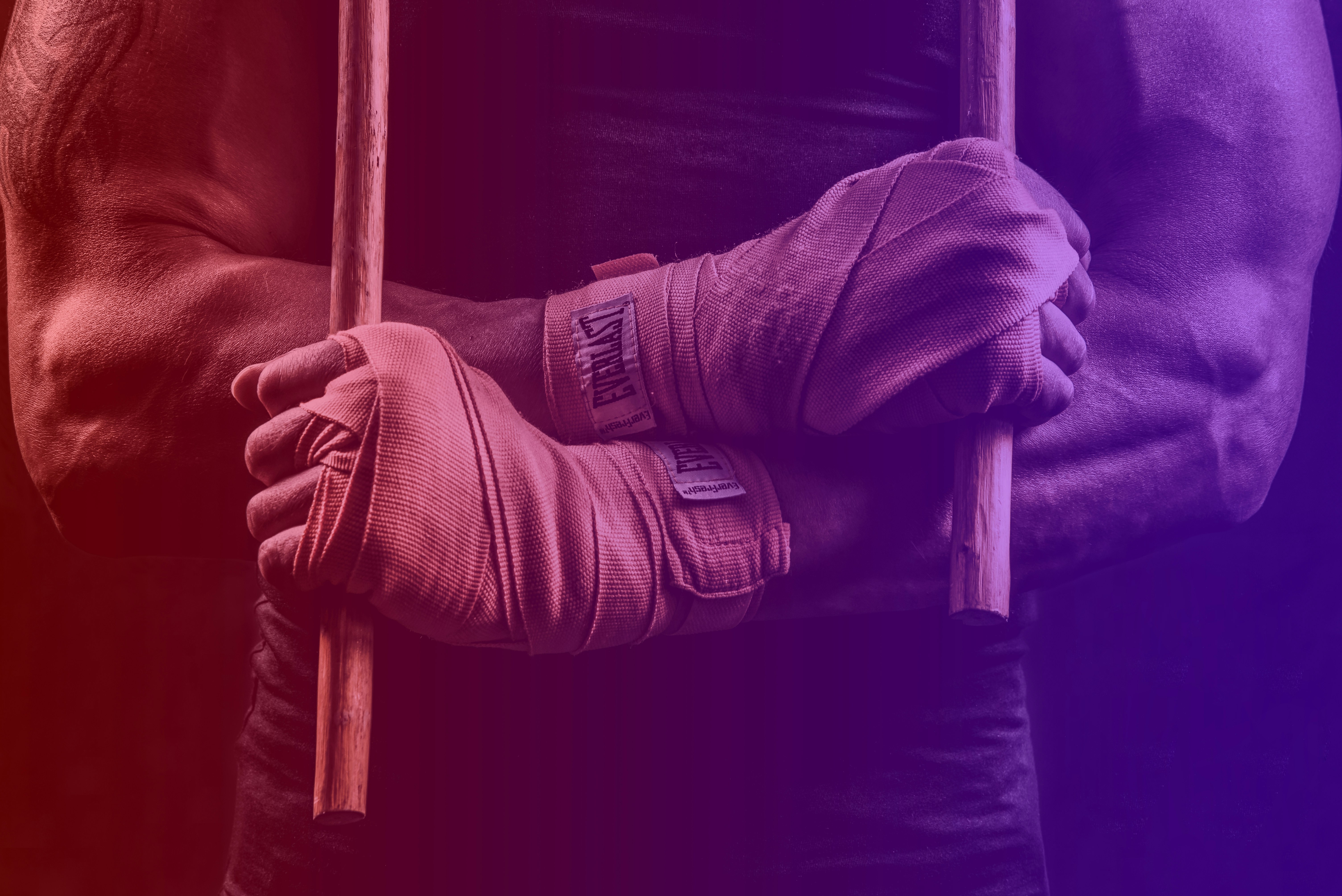 Paused clash: gloved fists grip a training bar in a moody studio
