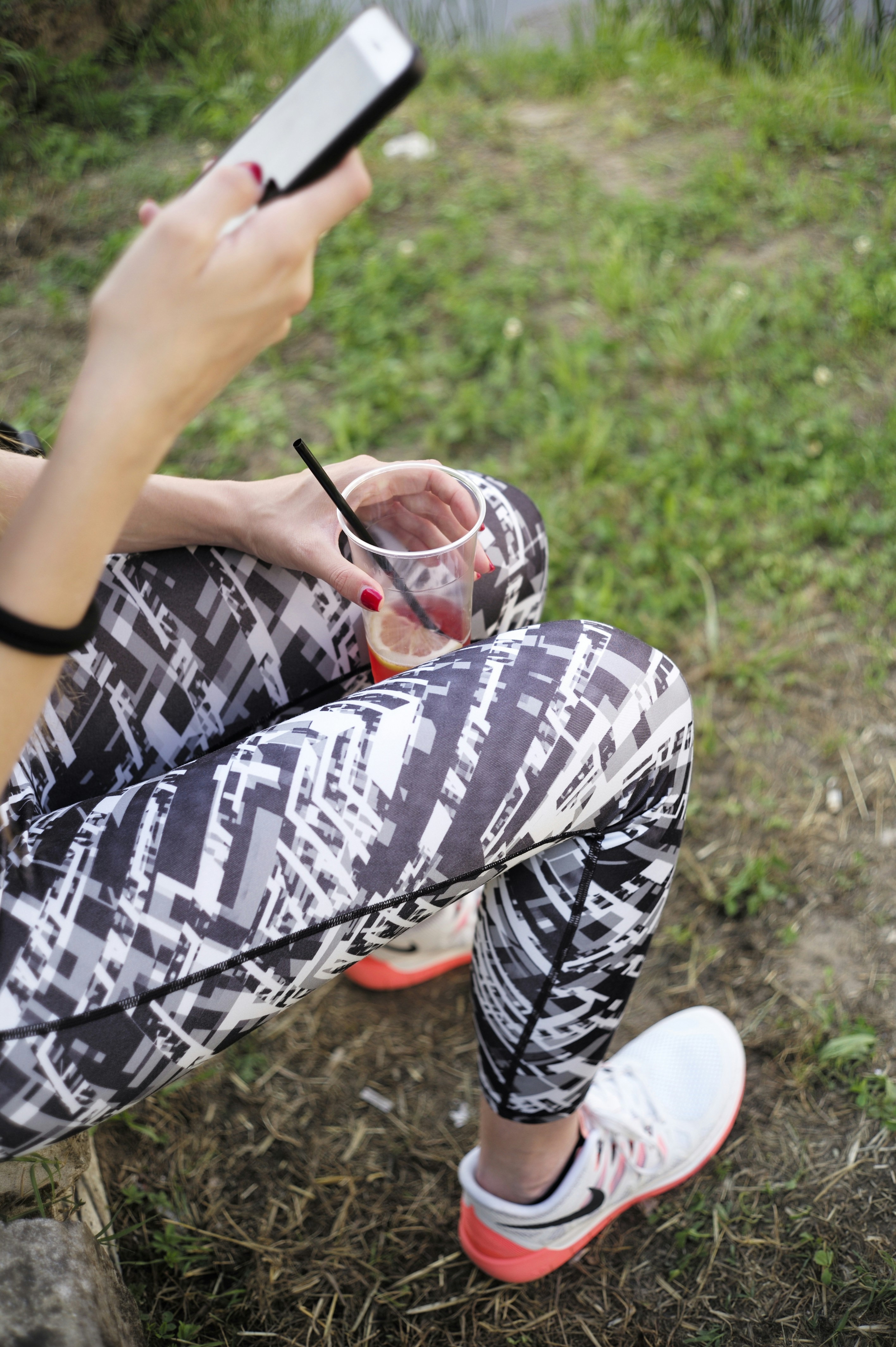 A woman seated outdoors, engaged with her smartphone while enjoying a drink, showcasing a blend of casual style and modern technology.