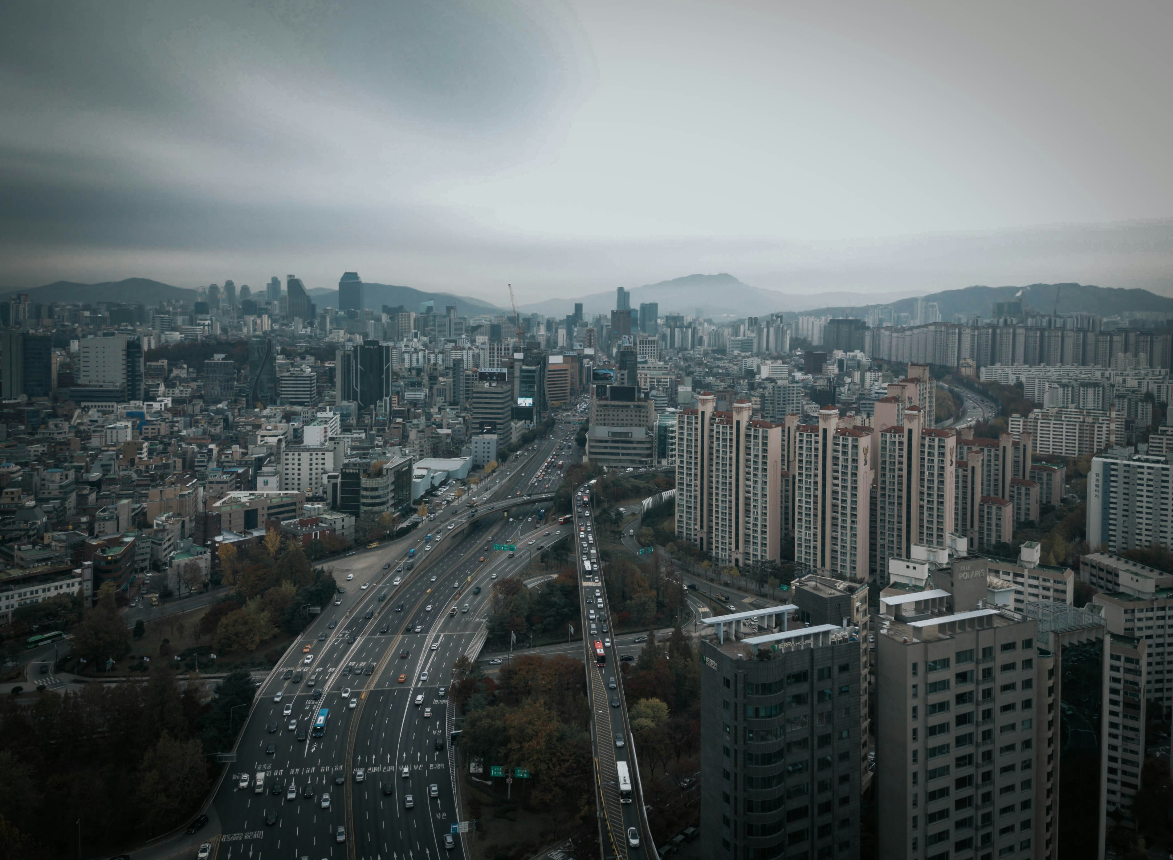 Aerial view of a bustling cityscape, showcasing a network of highways and towering buildings under a moody sky.