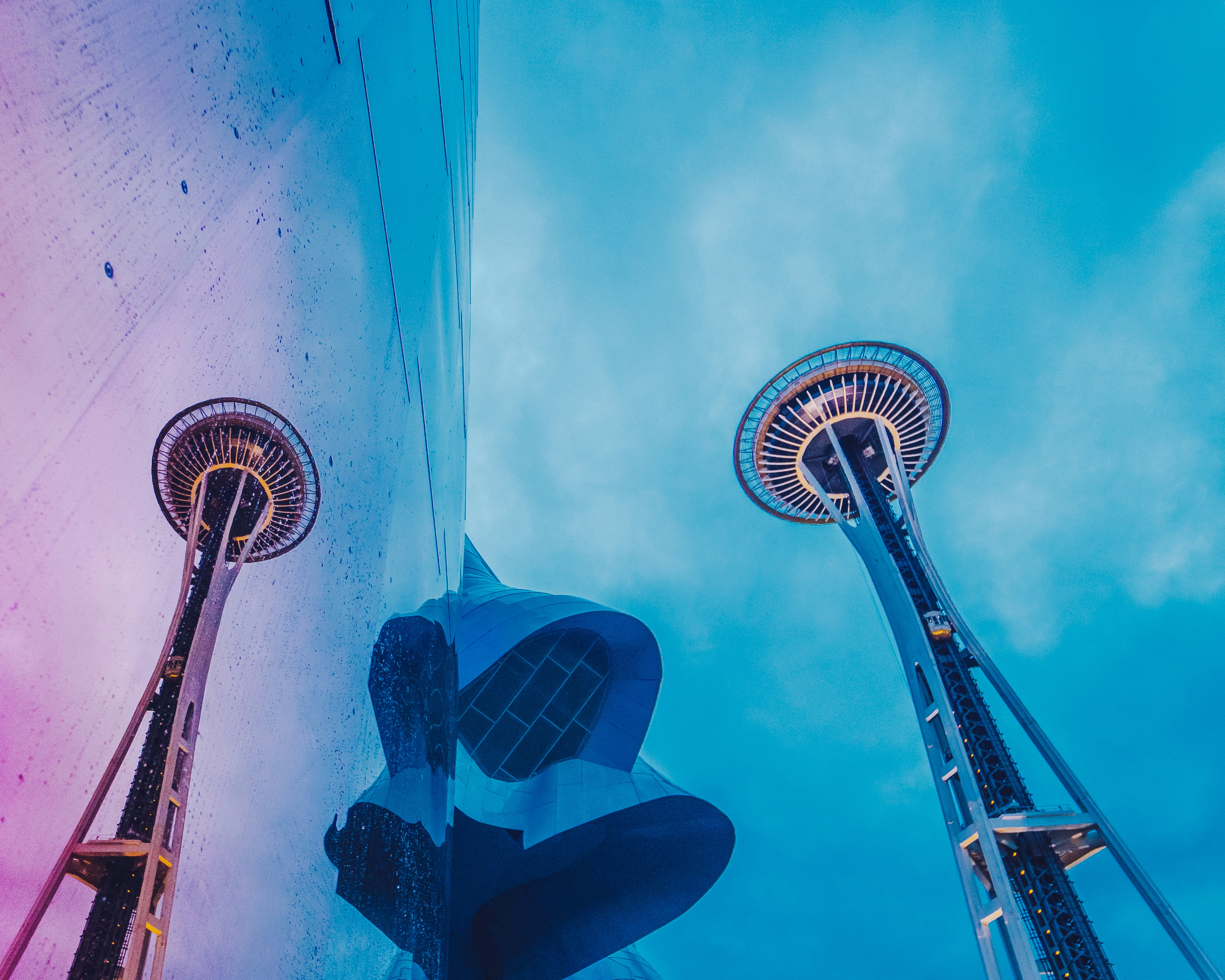 Modern tower reflected in a sleek building facade under a vivid blue sky.