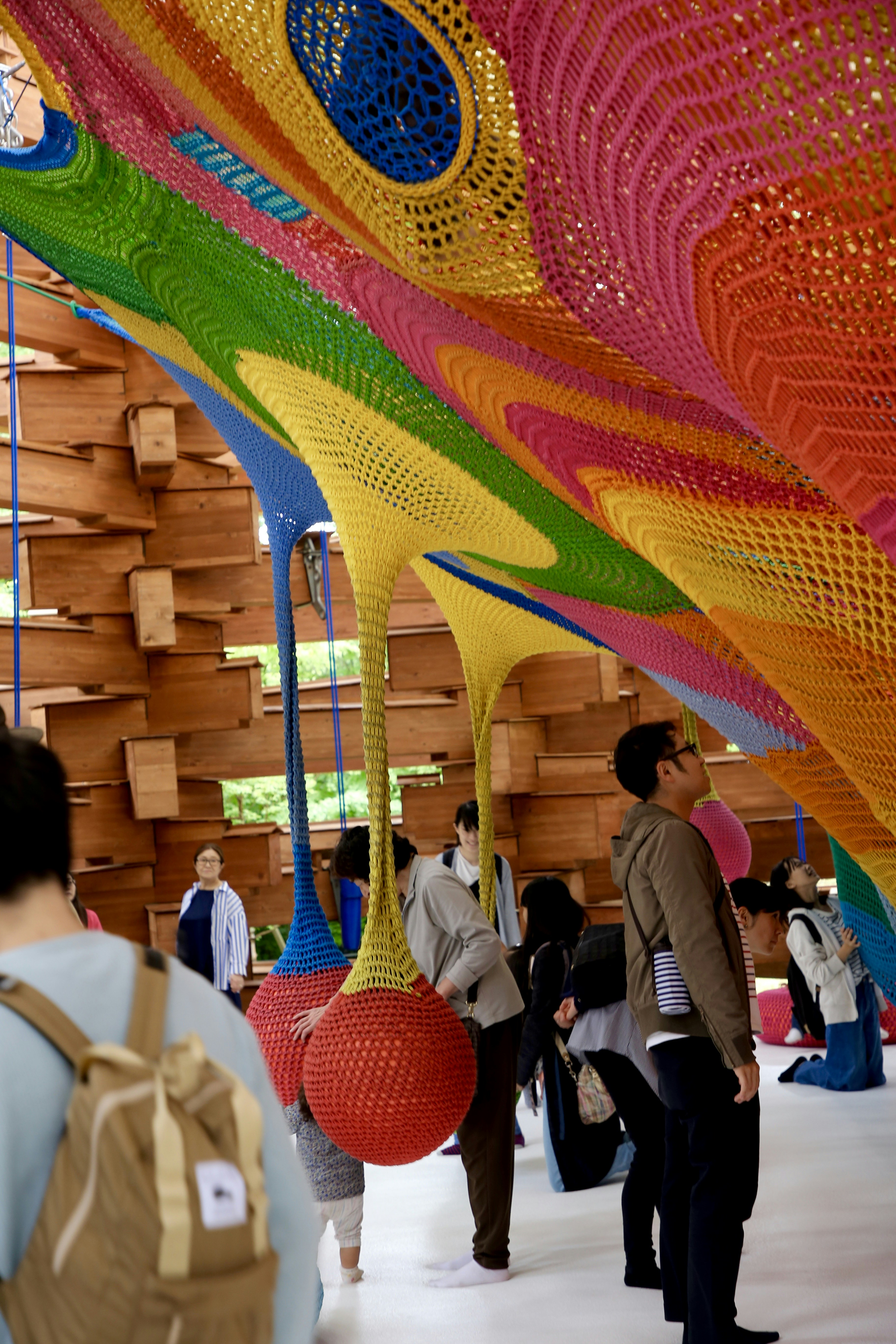 Rainbow Crochet Canopy Over a Wooden Atrium Filled with Visitors