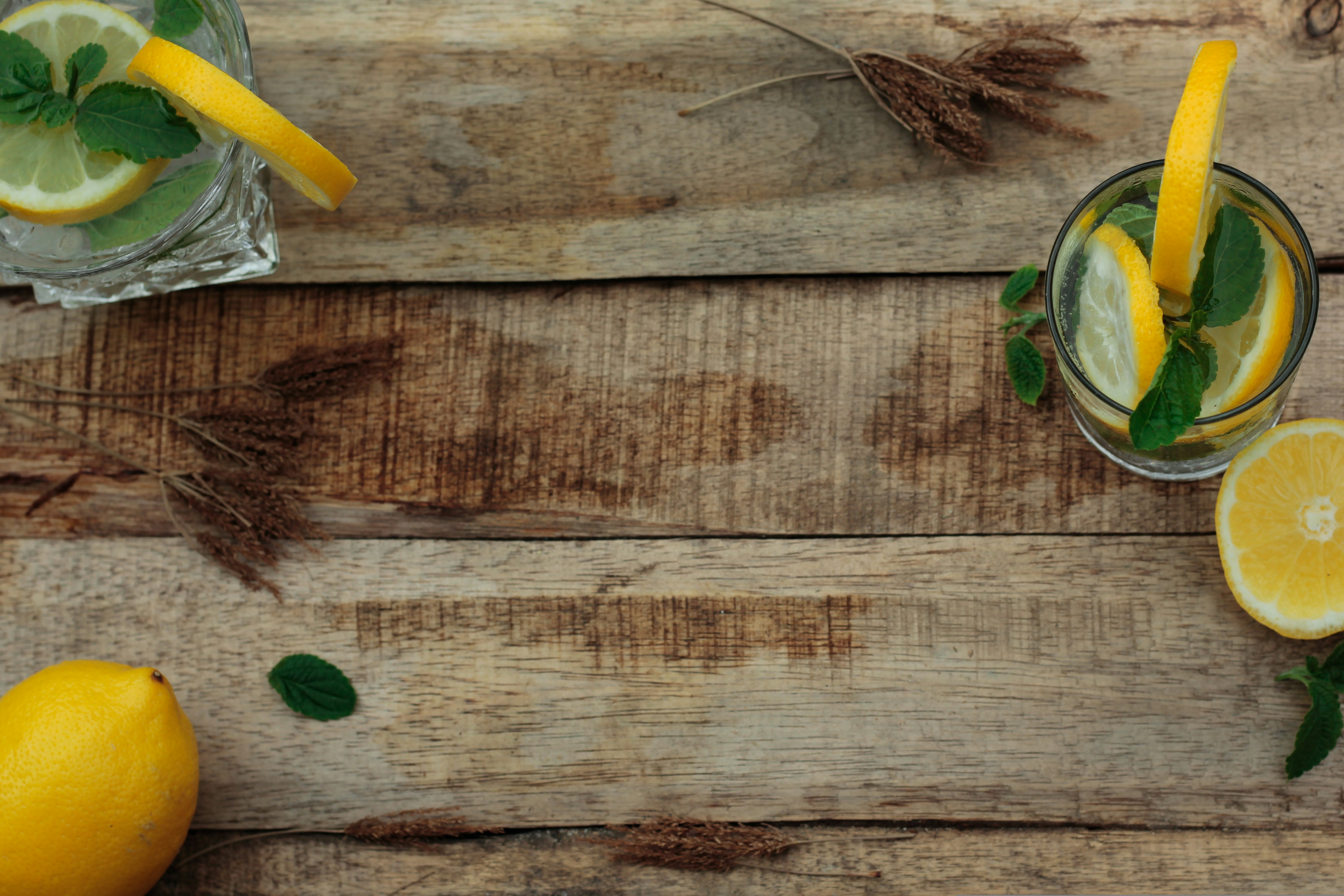 Glasses of lemon-infused water garnished with mint leaves, arranged on a weathered wooden surface, complemented by fresh lemons.