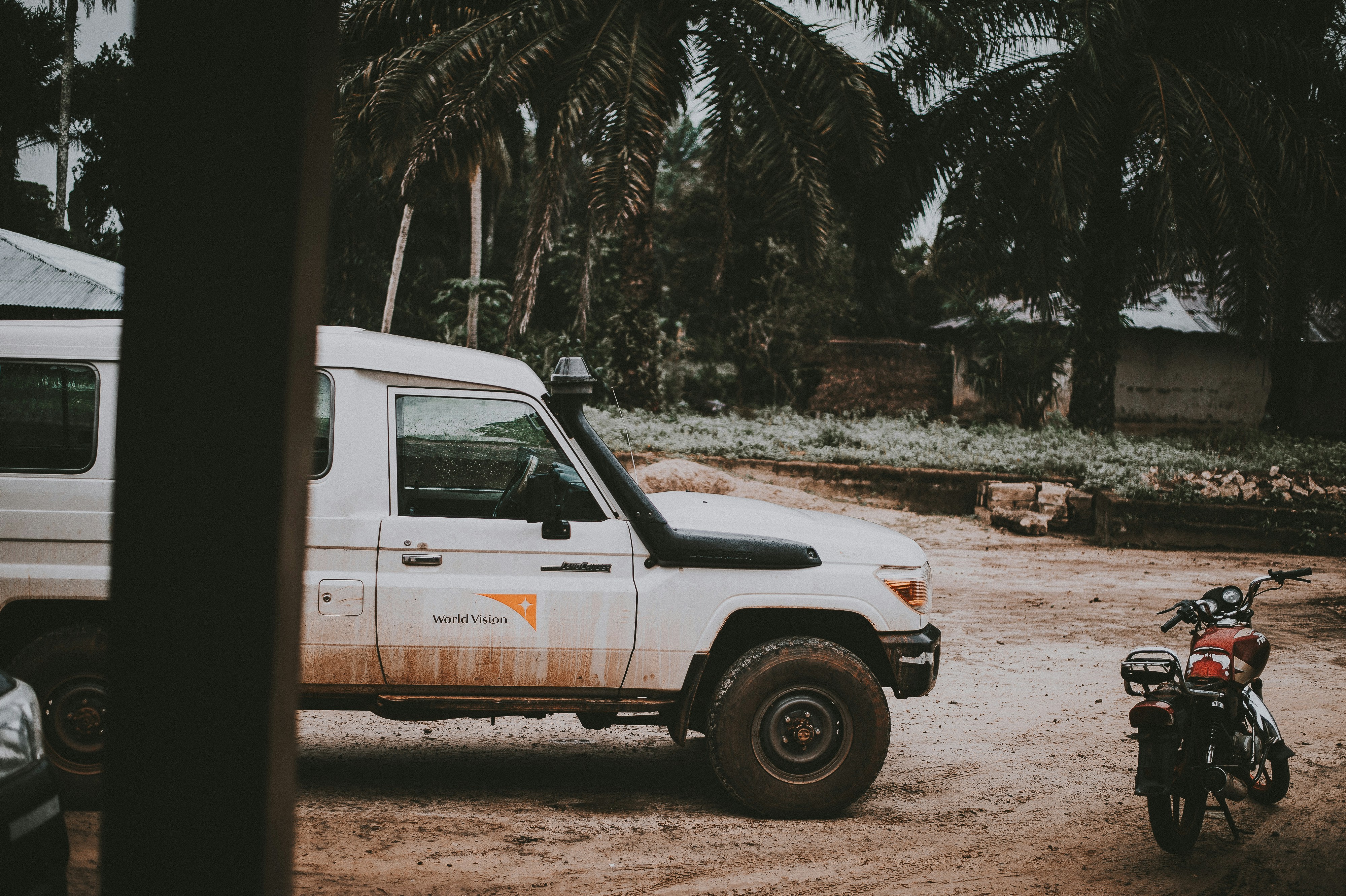 Dusty Yard Dialogue: A Weathered Van and a Quiet Motorcycle Under Palm Shade