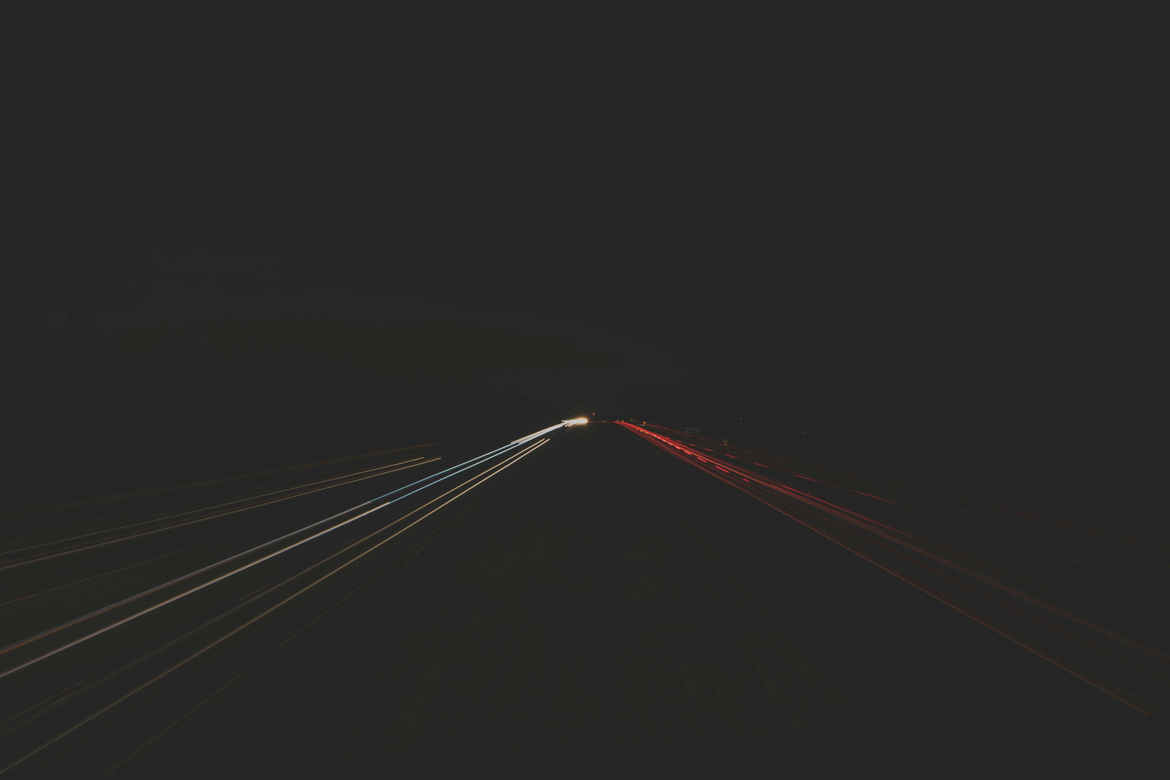 Long exposure of car light trails on a highway at night, creating dynamic red and white streaks against a dark sky.
