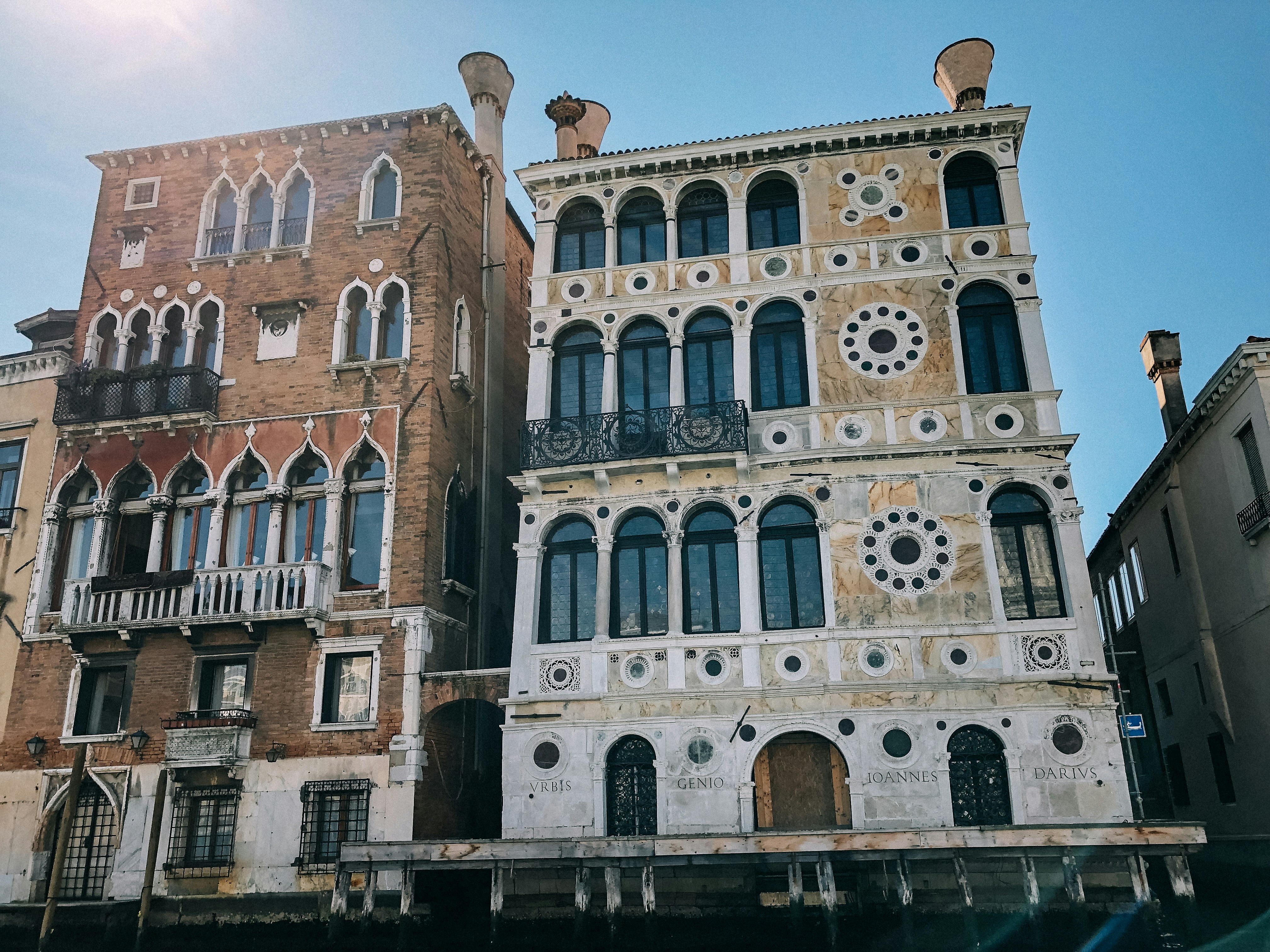 Two distinct Venetian buildings showcase contrasting architectural styles along a canal, highlighting the rich history and artistry of the city.