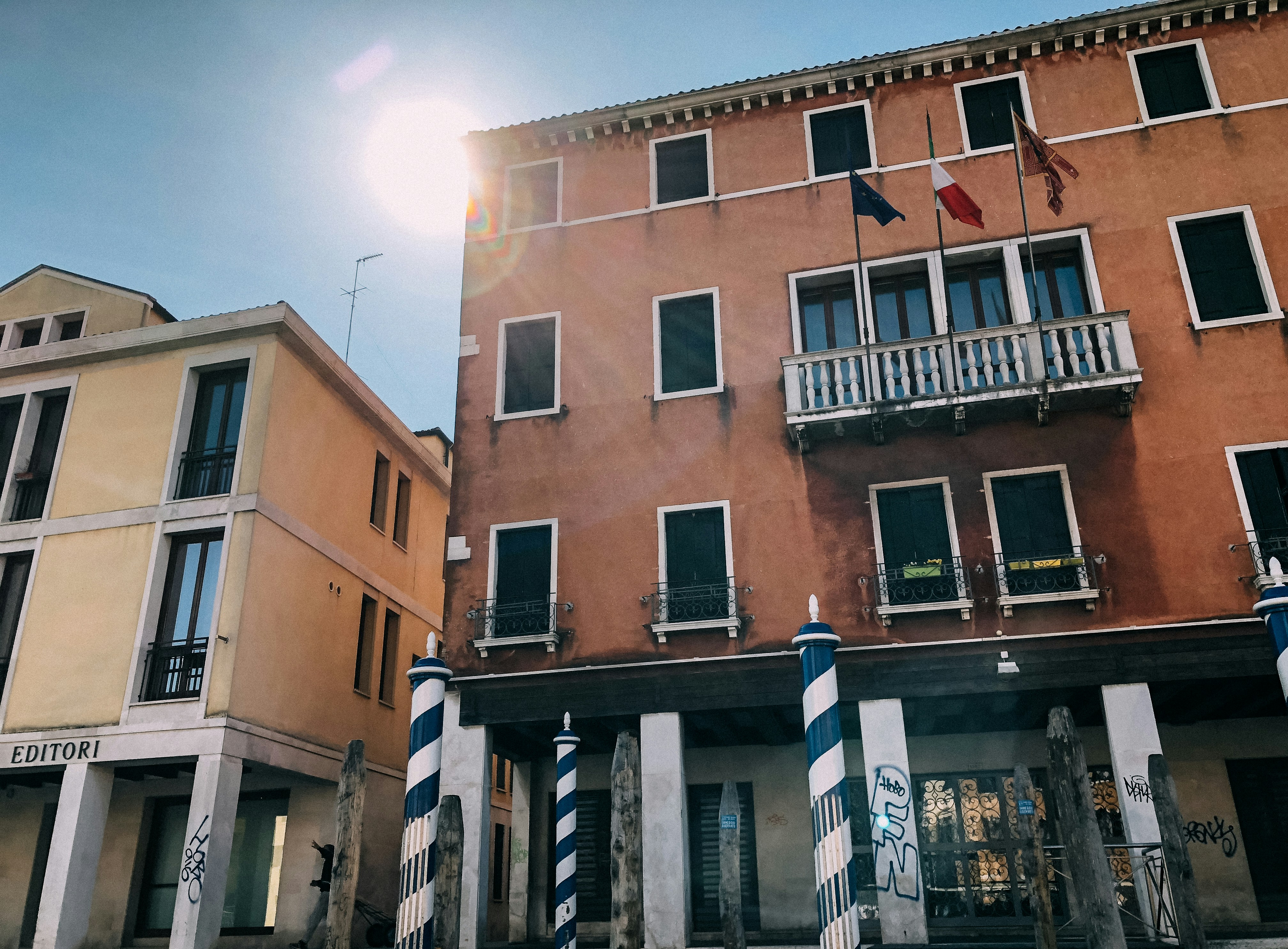 Sunlit Orange Facade Framed by Striped Poles and a Flag-Adorned Balcony