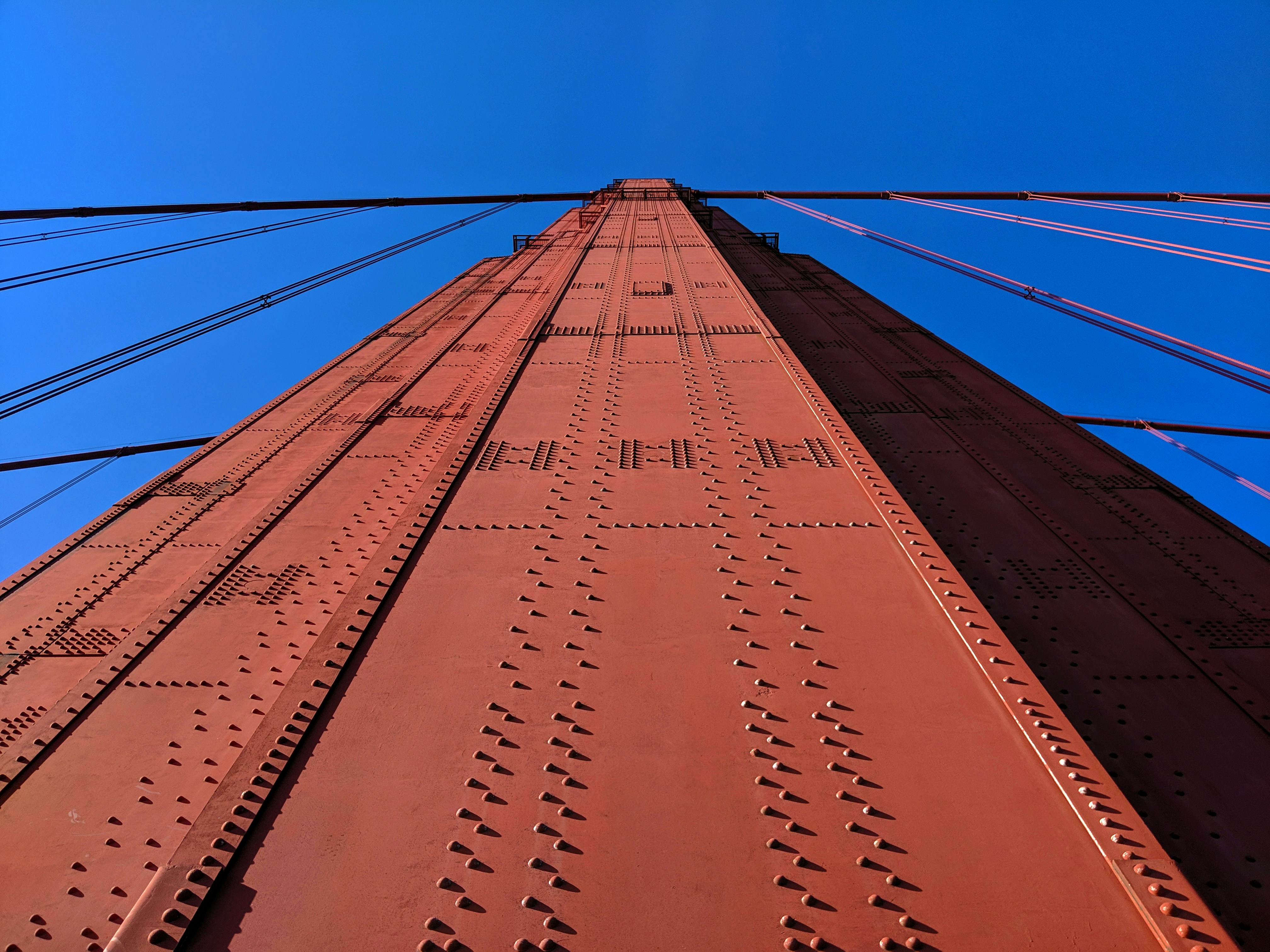 Looking up at the intricate structure of a towering suspension bridge against a clear blue sky.