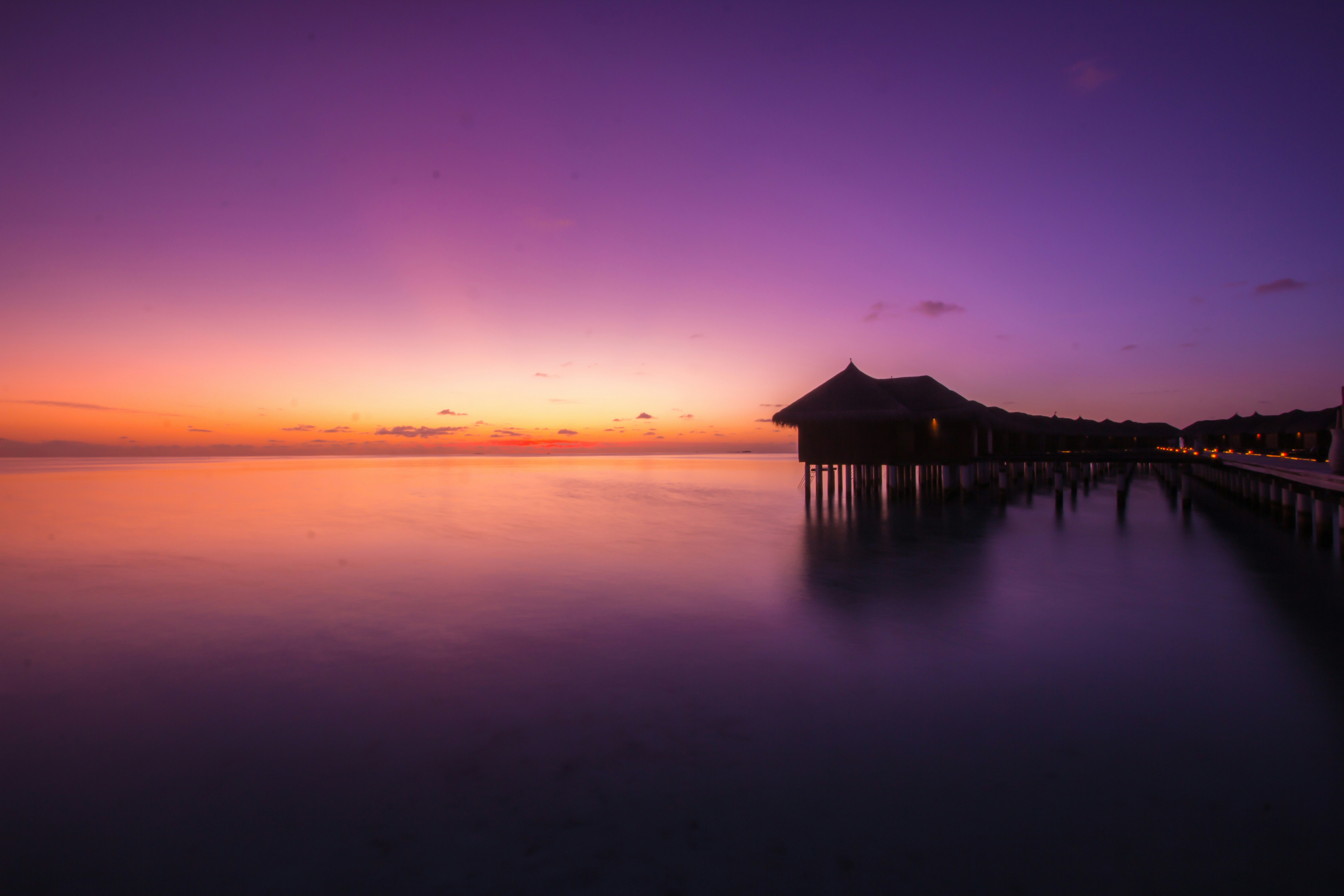Purple-hued sky reflecting on calm waters with silhouettes of overwater villas at dusk.