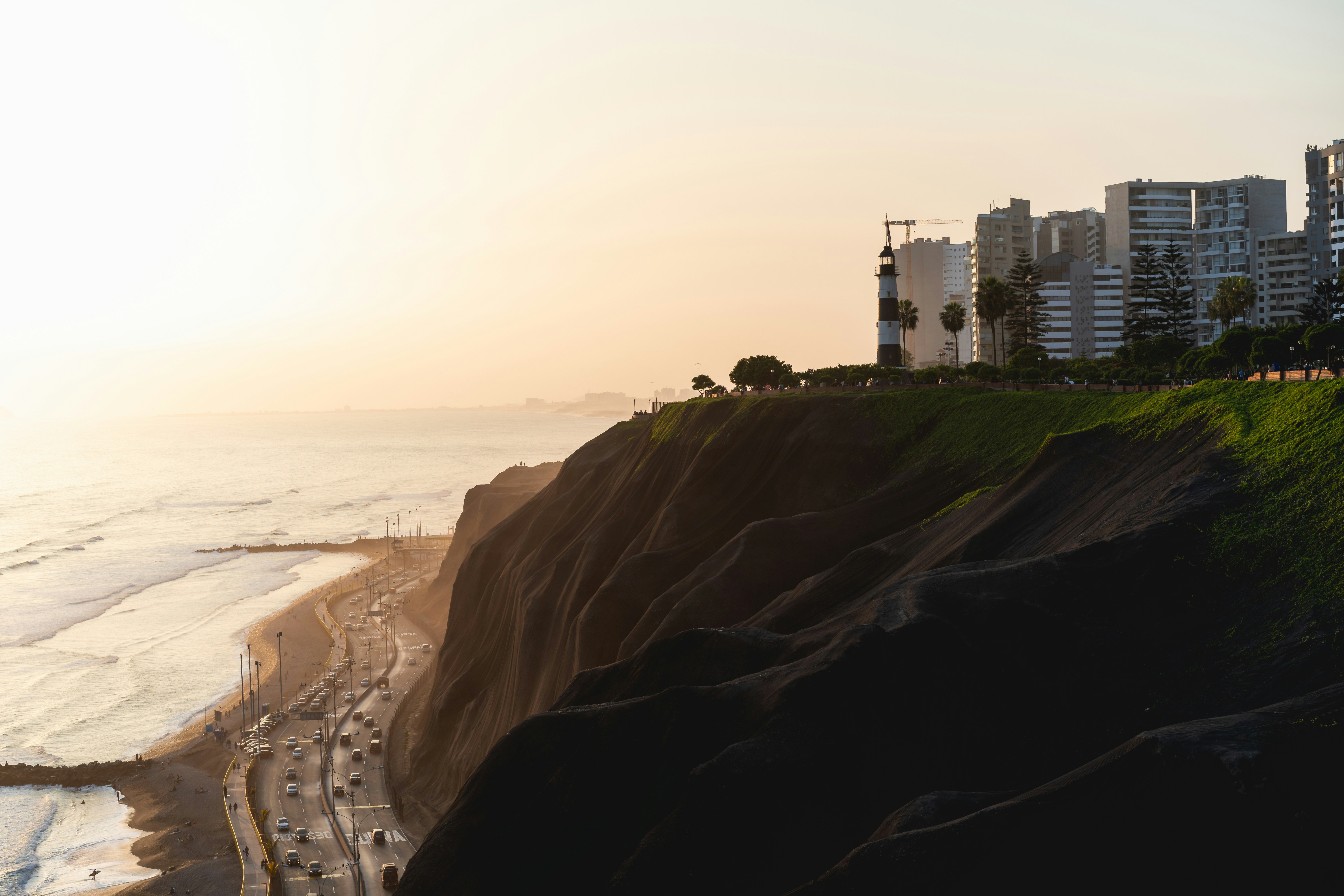 Tall cliffs overlooking a sunlit ocean with a line of modern buildings along the edge.