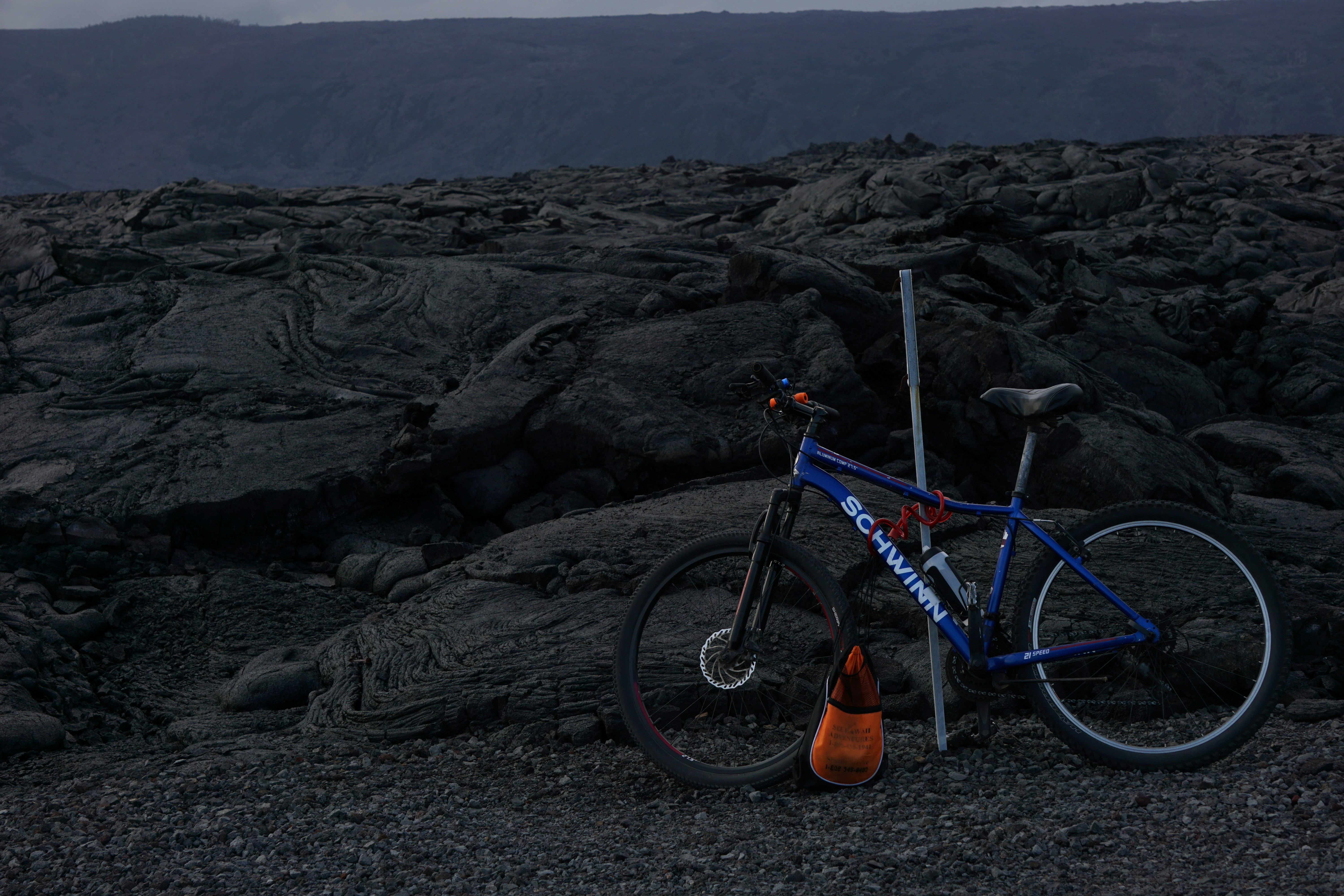 Blue Mountain Bike Resting on Volcanic Shore with Orange Cone