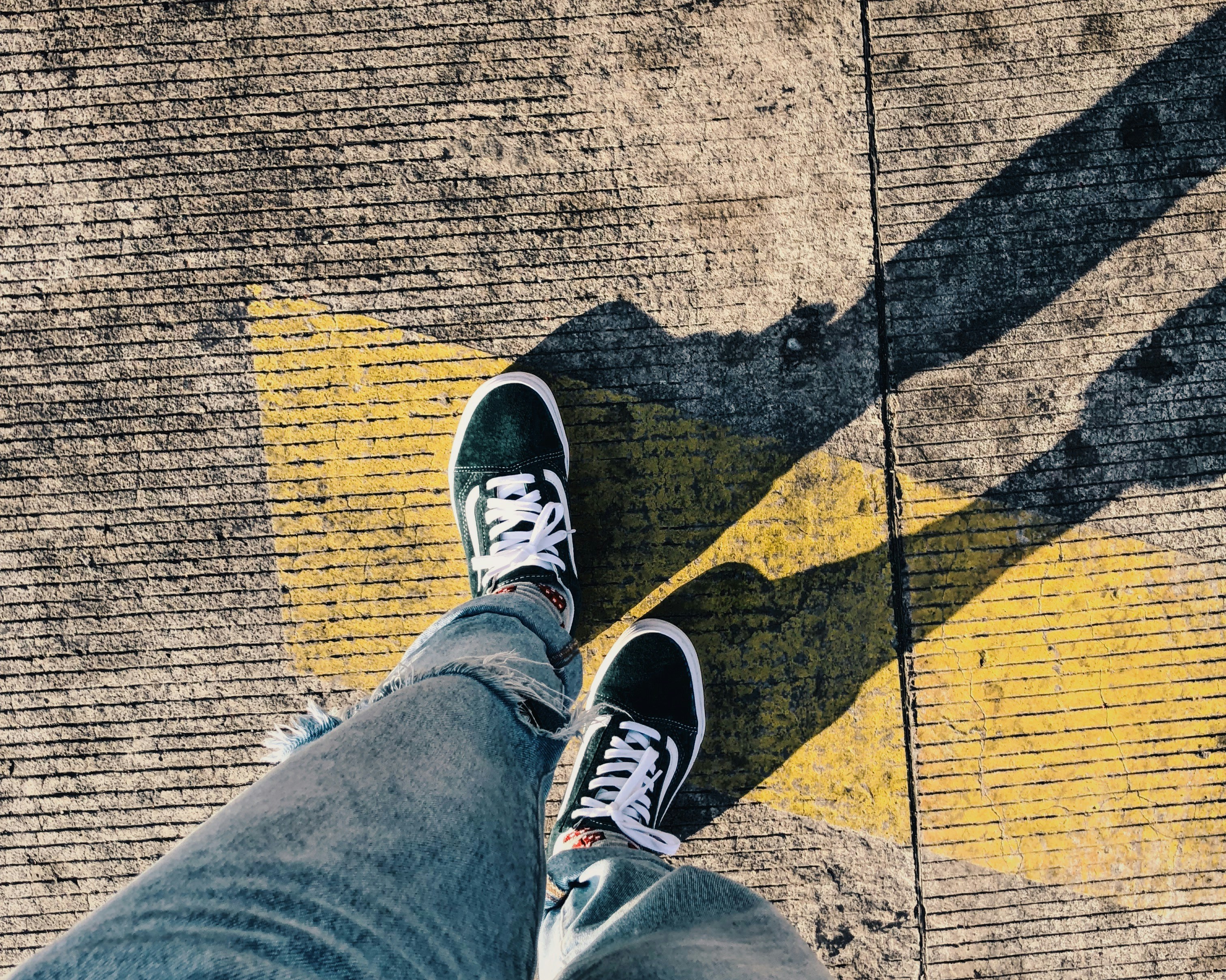 A pair of sneakers resting on a textured surface, casting a shadow over a vibrant yellow arrow on the ground.