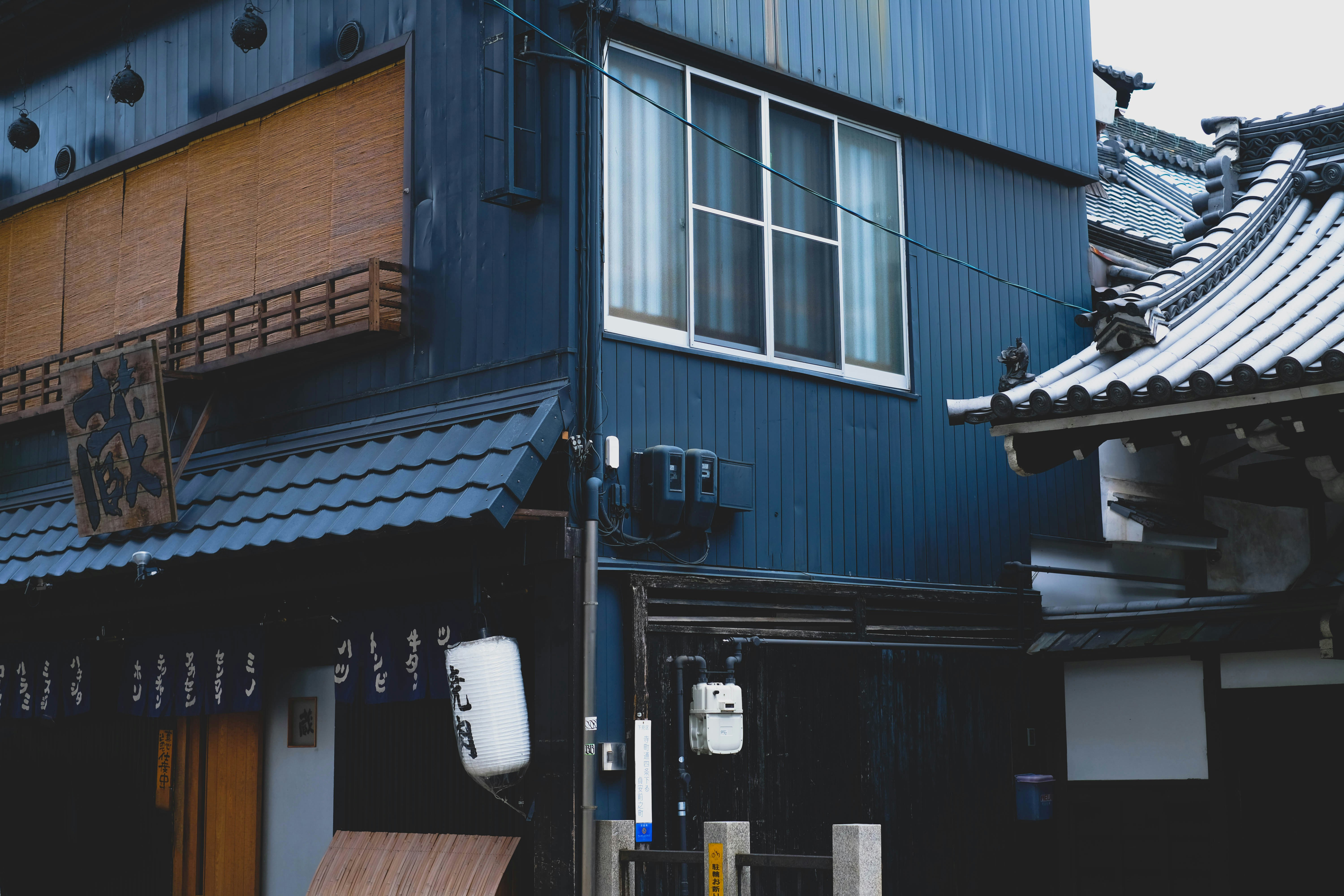 Historic building with a dark blue facade, featuring traditional wooden elements and a paper lantern, nestled among tiled rooftops.