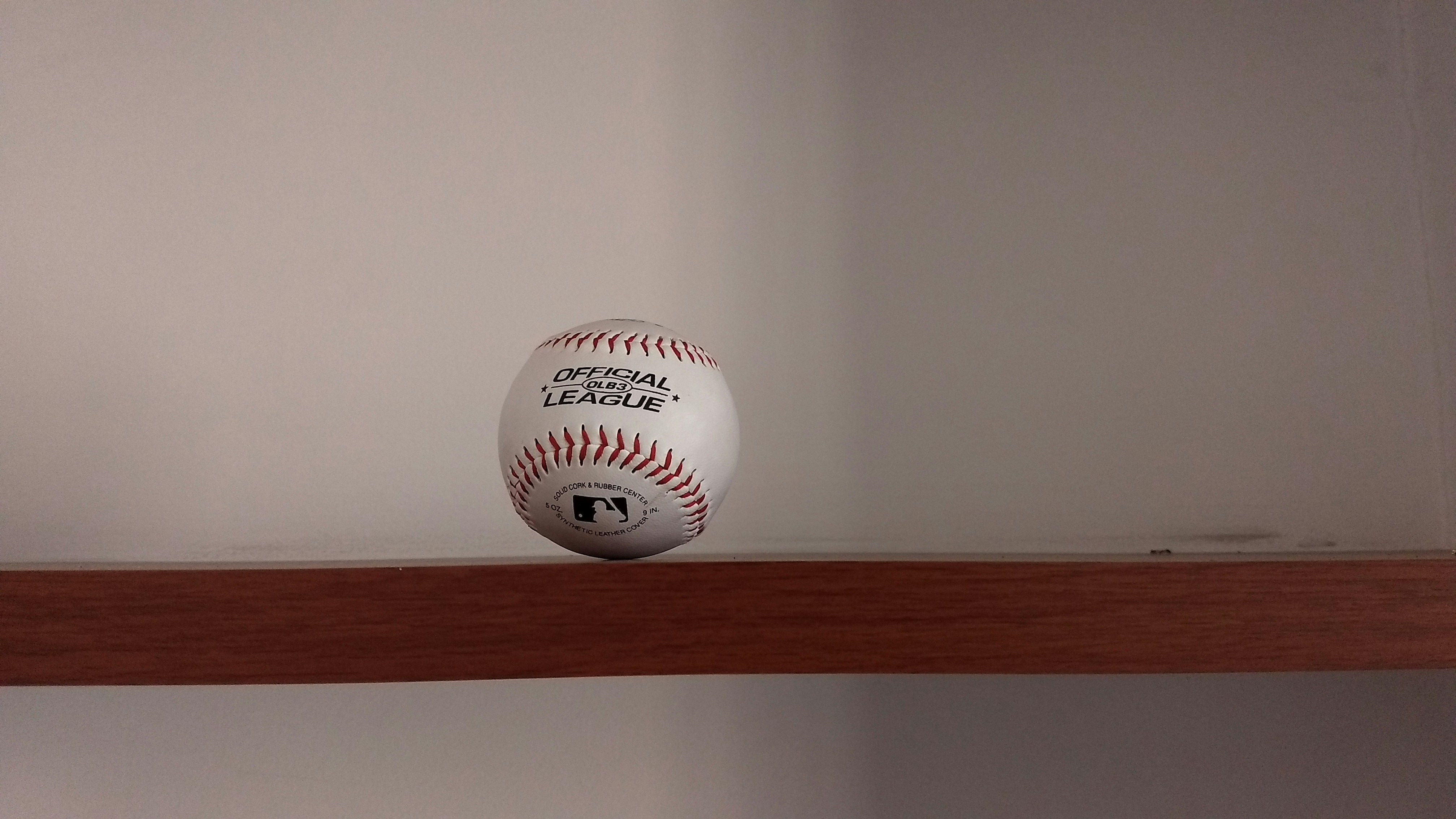 Baseball resting on a wooden shelf, showcasing its detailed stitching and logo against a minimalist background.