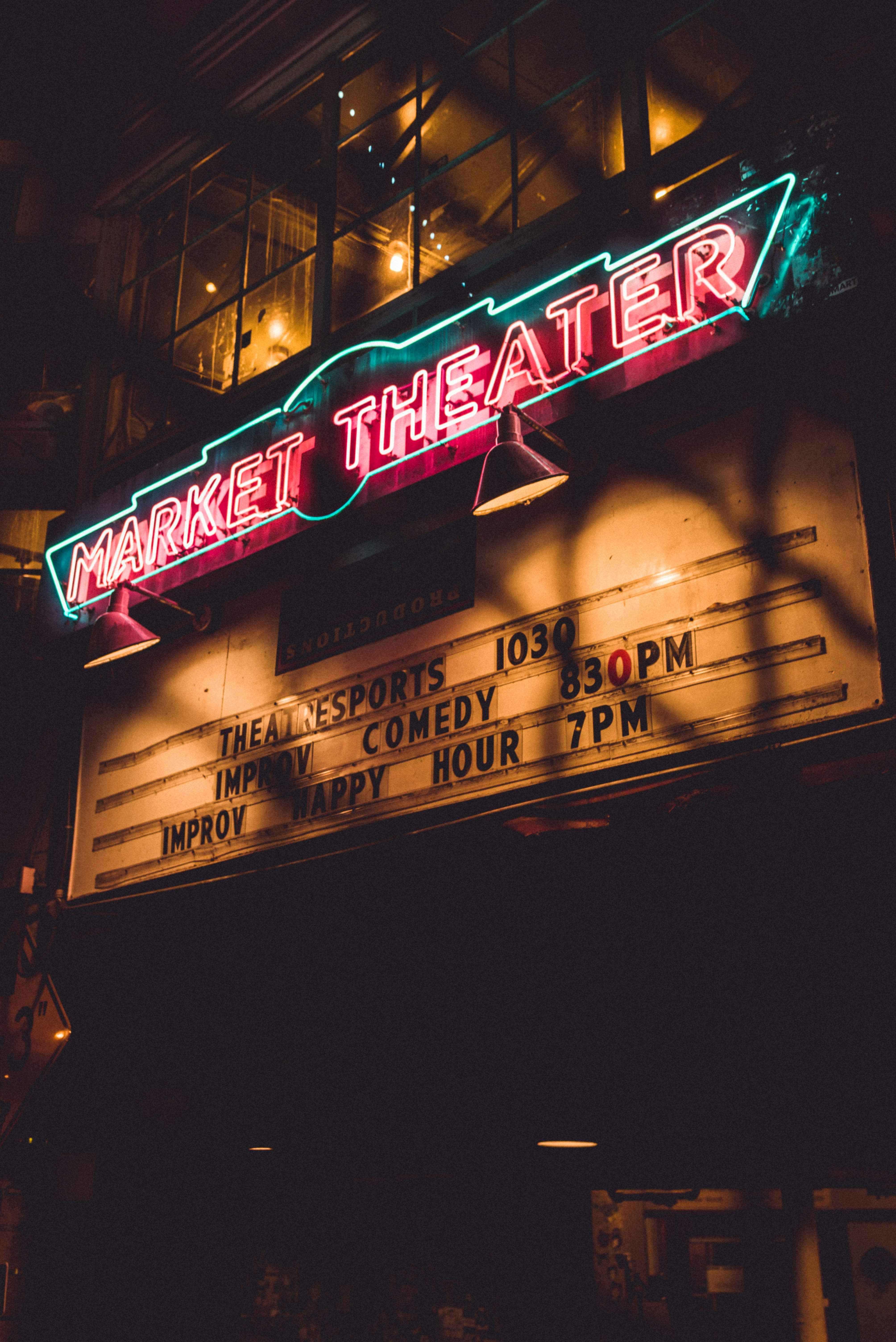 Vibrant neon sign of the Market Theater illuminates the evening, showcasing upcoming events on its marquee.