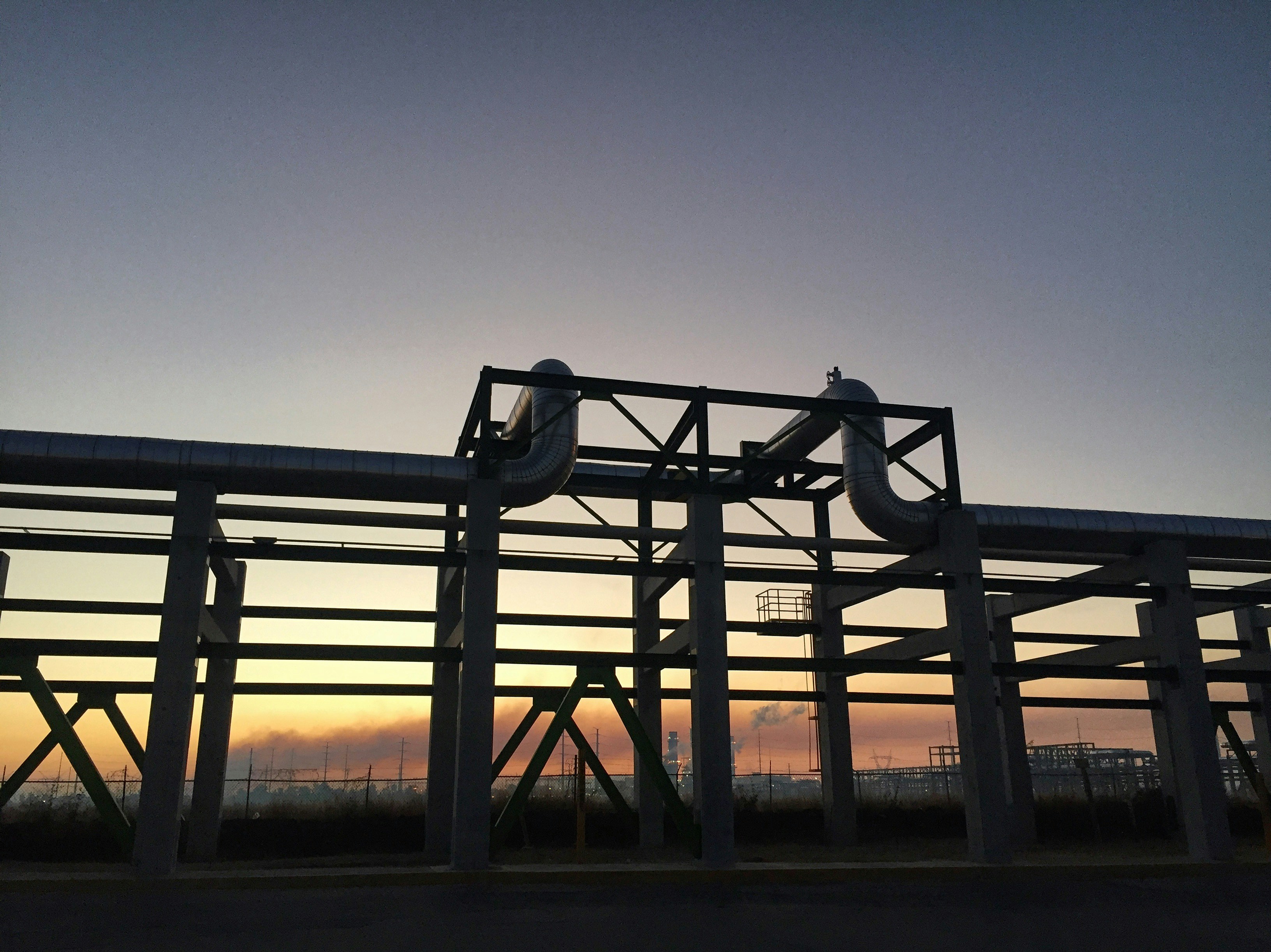 Silhouetted metal pipes under a vibrant blue and orange sky during twilight.