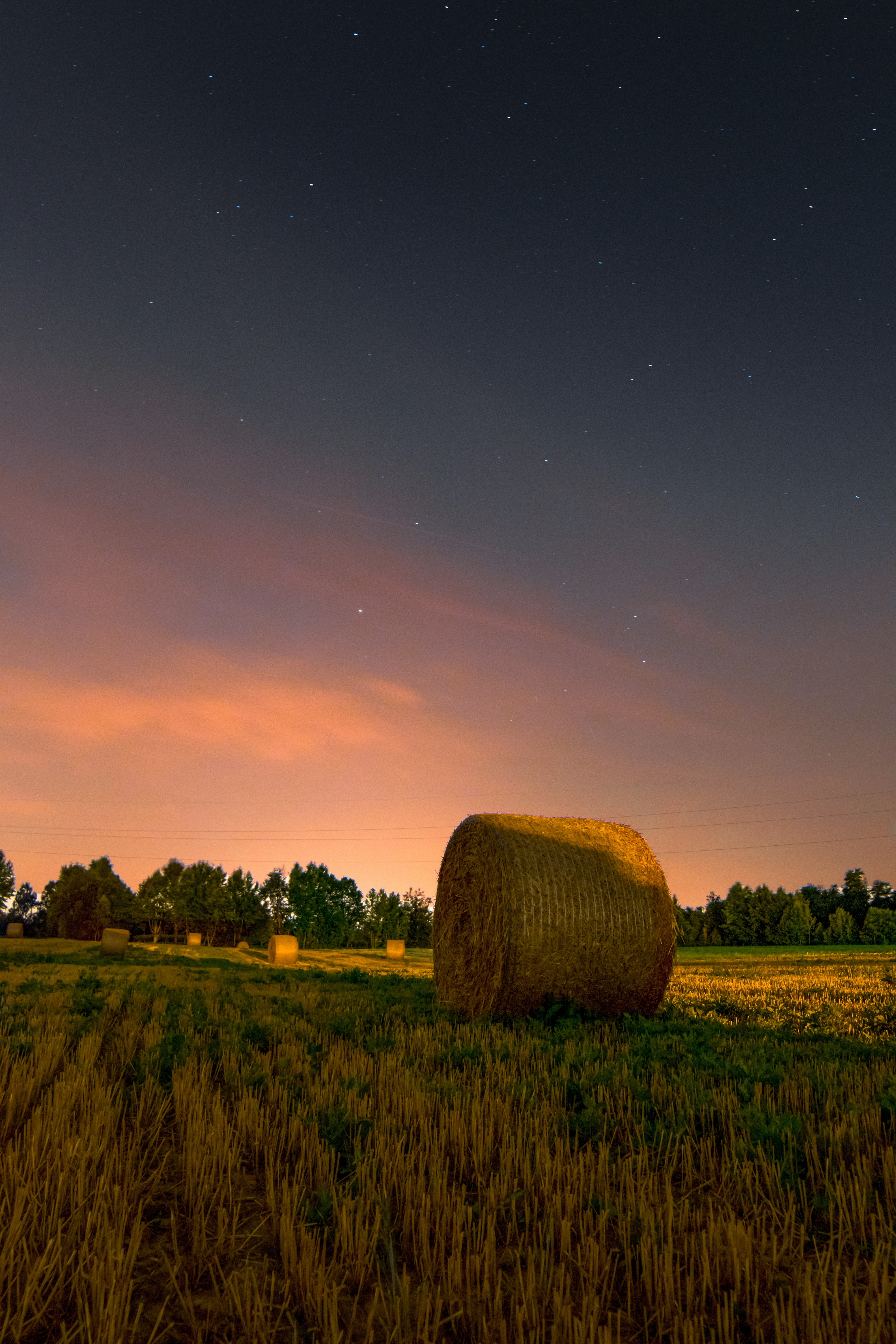 Amber Horizon Over a Lone Hay Bale Beneath a Starry Field