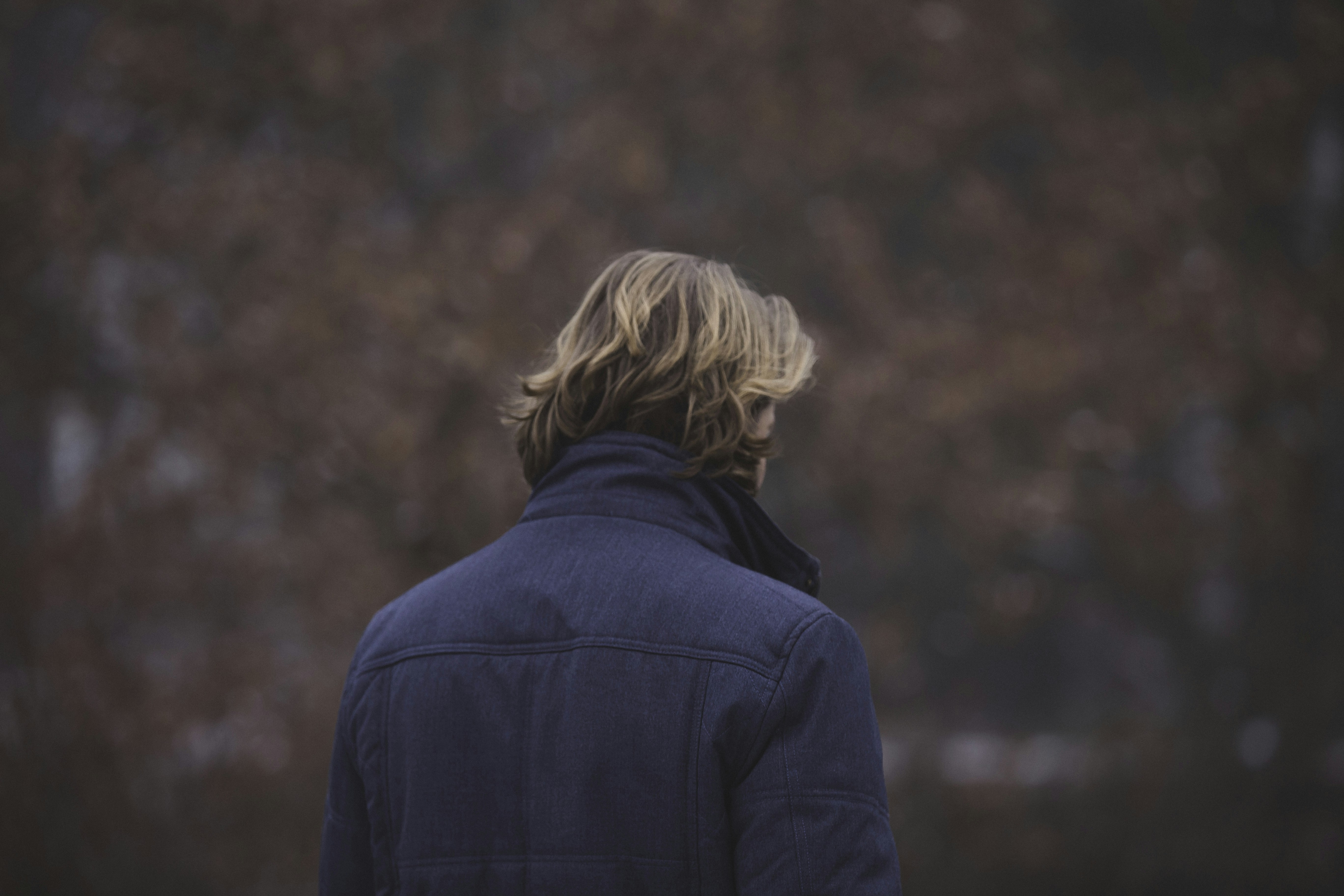 Person in a dark jacket facing away, set against a backdrop of blurred autumn foliage.