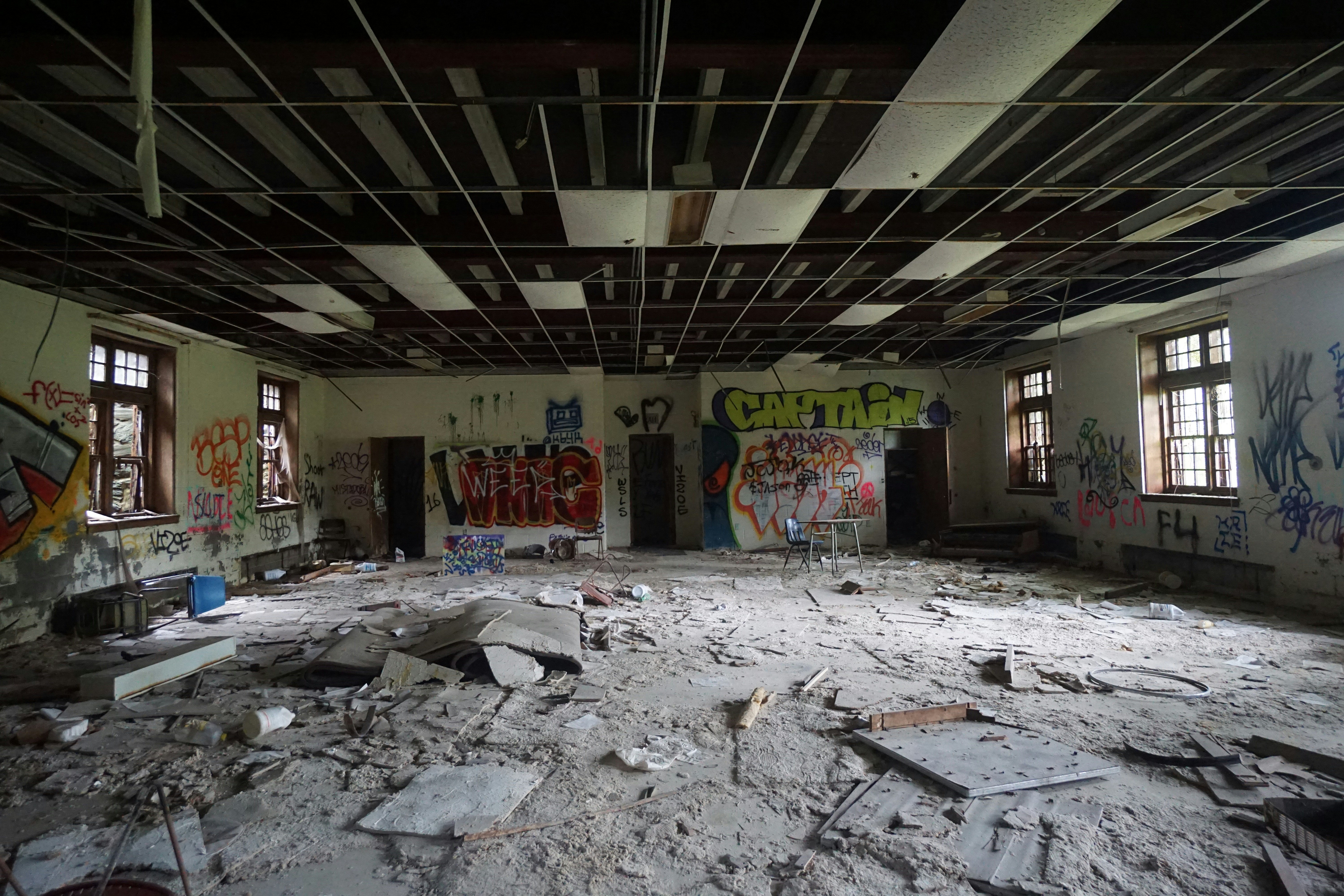 An abandoned room filled with debris and vibrant graffiti, showcasing the remnants of a forgotten space. The walls tell stories through colorful tags and messages.