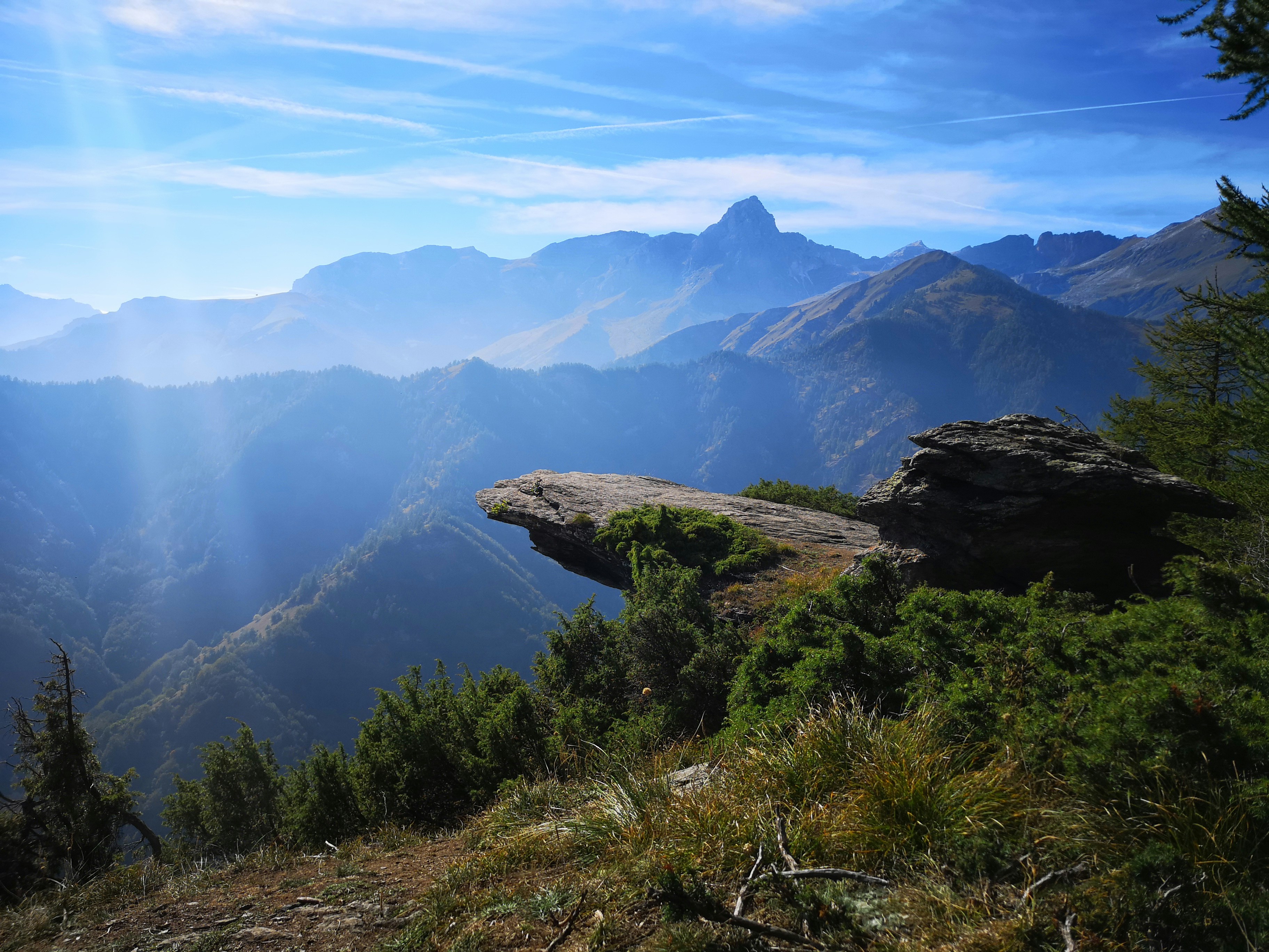 Rocky outcrop overlooking misty mountain range under blue sky.