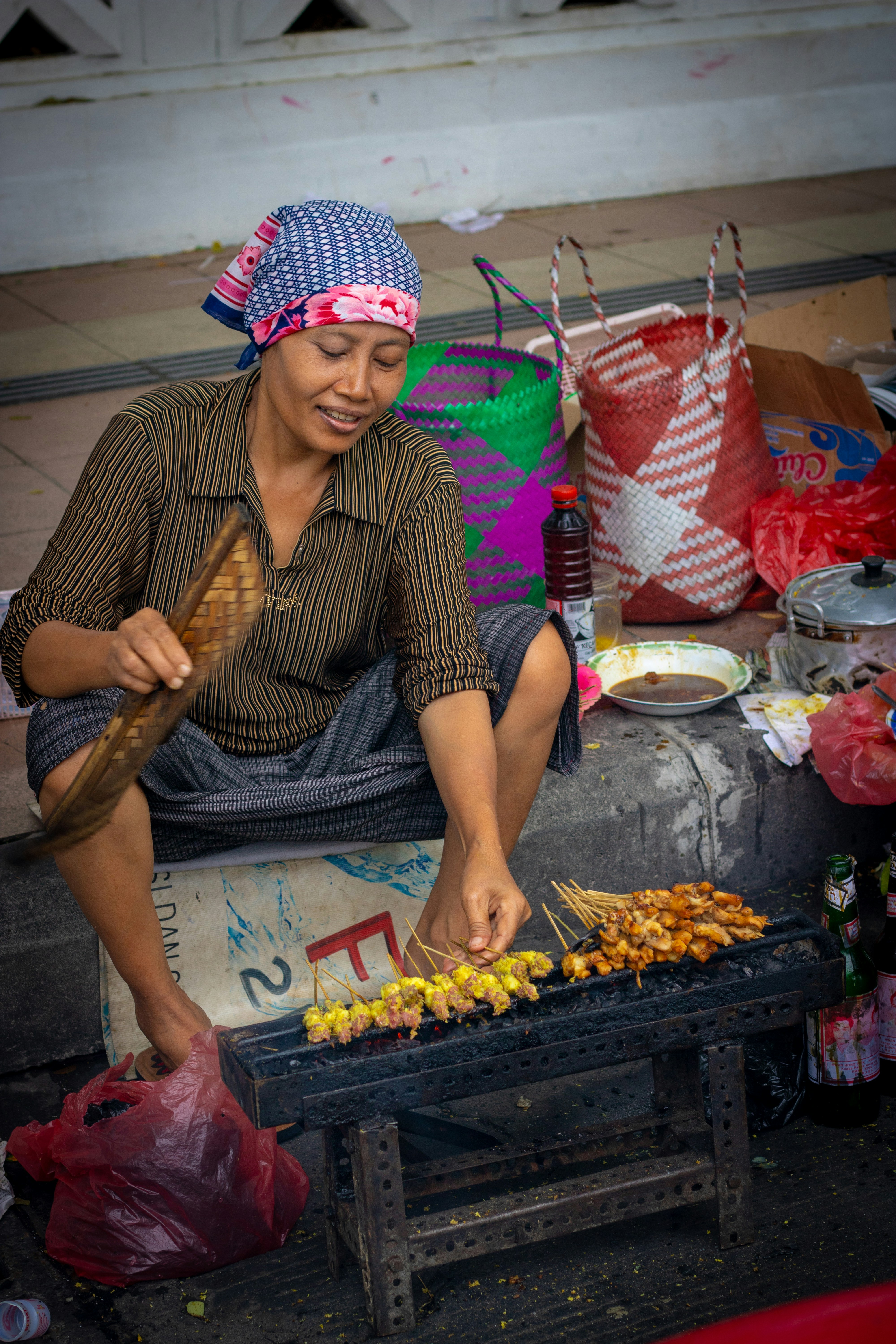 A street vendor meticulously preparing skewers of grilled meat and vegetables, surrounded by colorful baskets and cooking utensils.