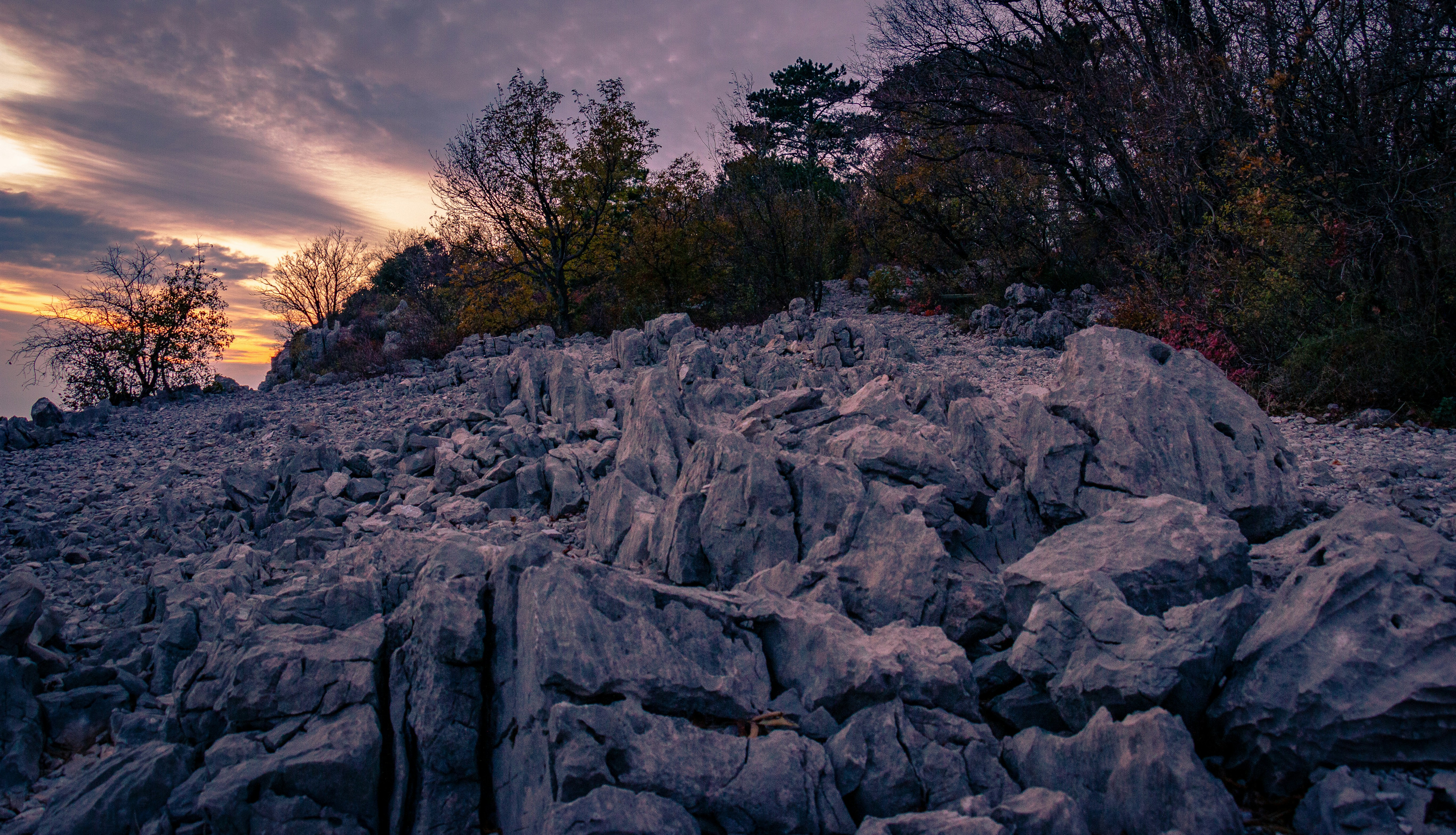 Craggy limestone formations under a vibrant dusk sky with silhouetted trees on the horizon.