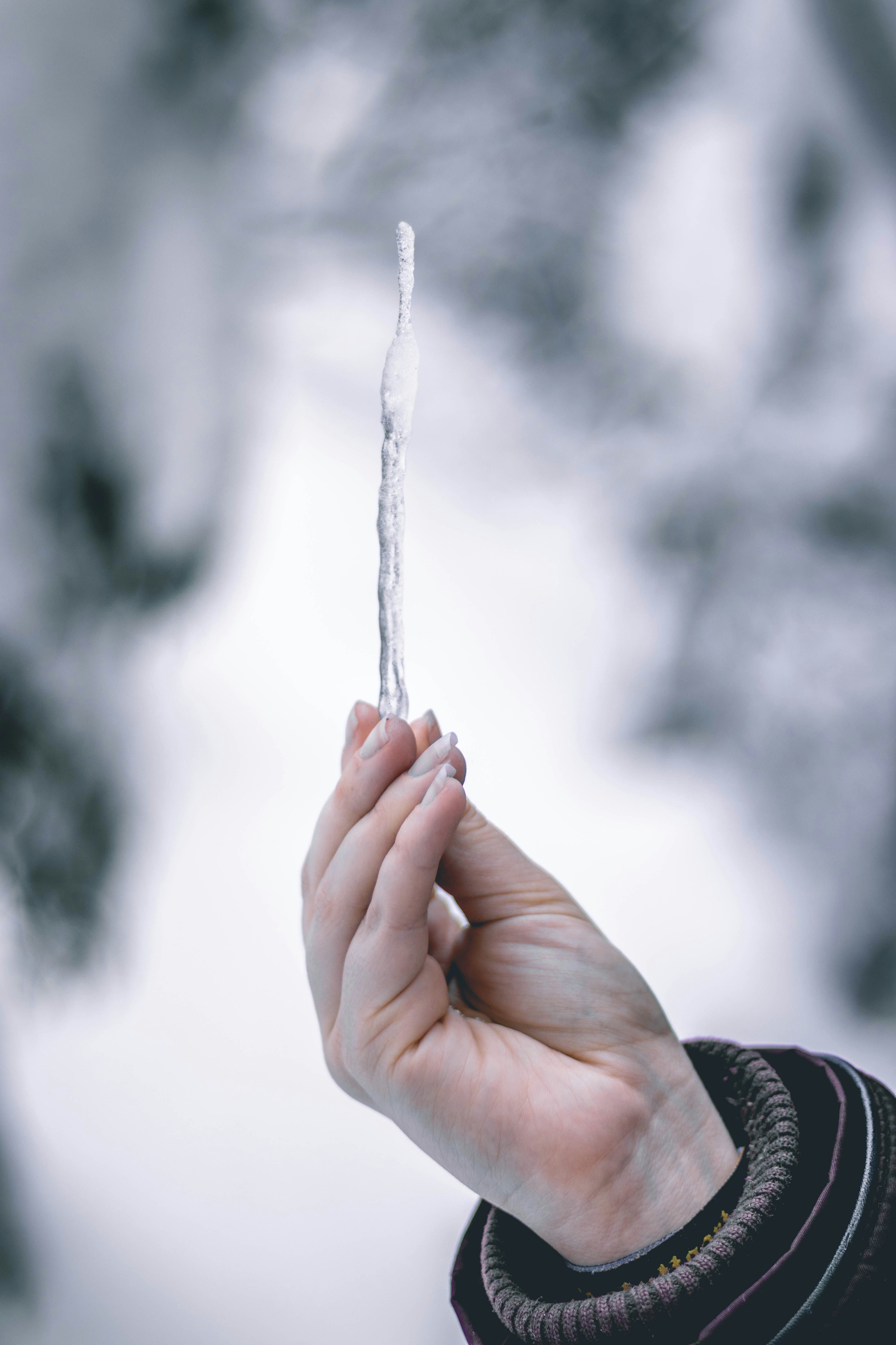 A hand gracefully holds a slender icicle against a blurred winter backdrop. The soft focus enhances the icy detail, highlighting the contrast between warmth and cold.