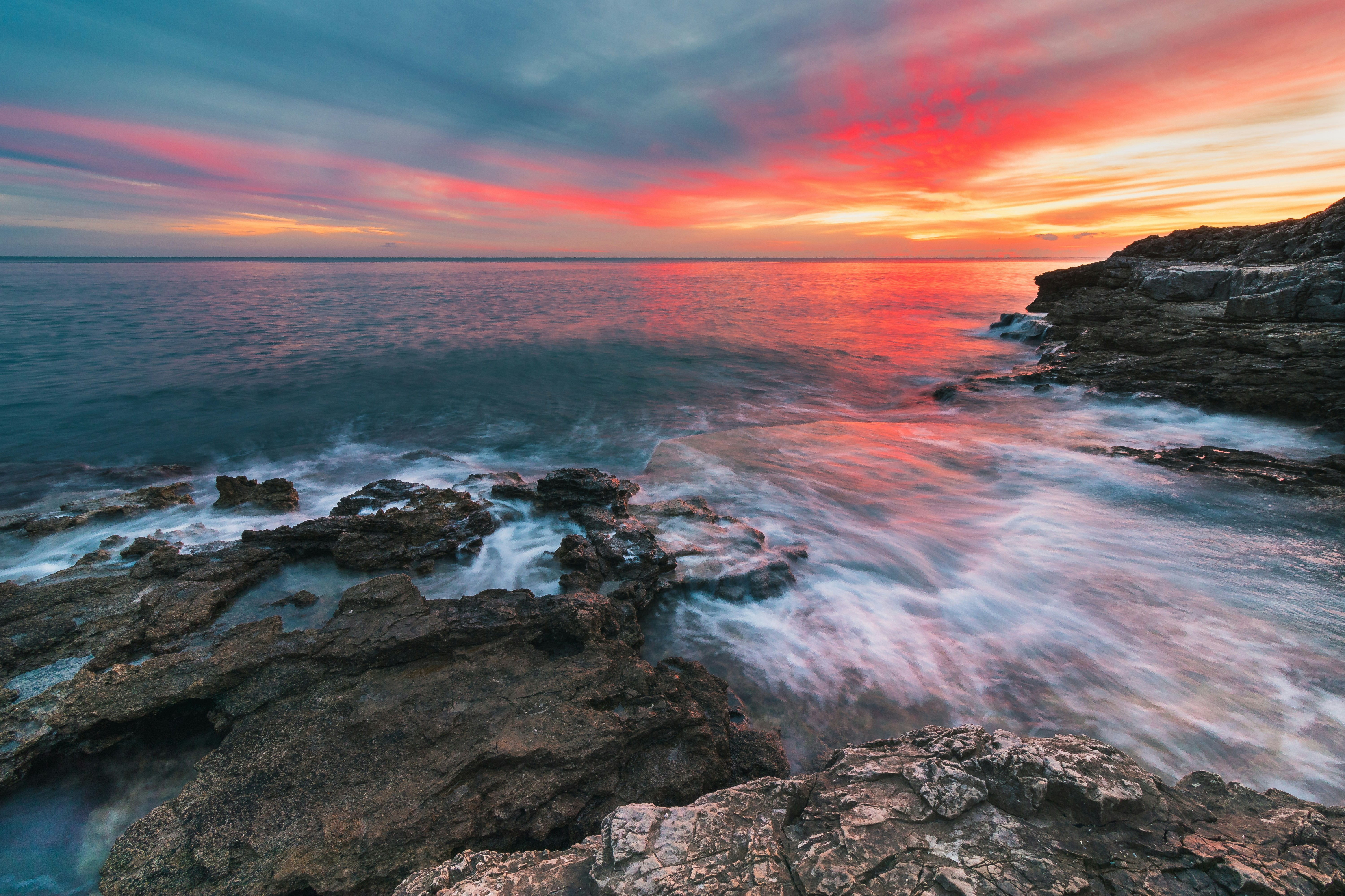 Rocky shoreline with vibrant sunset reflecting on ocean waters.