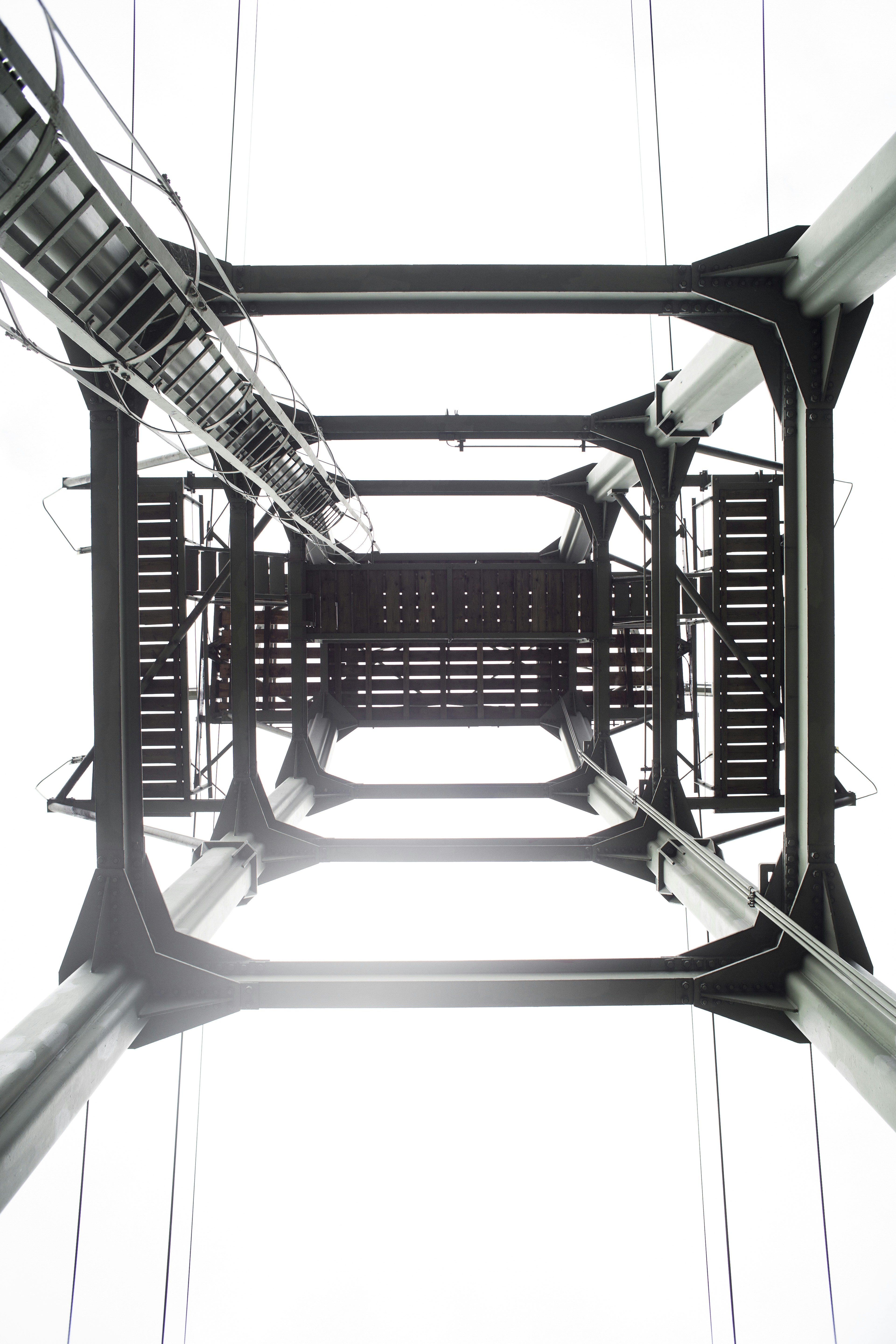 View from below a tall structure, showcasing its intricate metal framework against a bright sky.