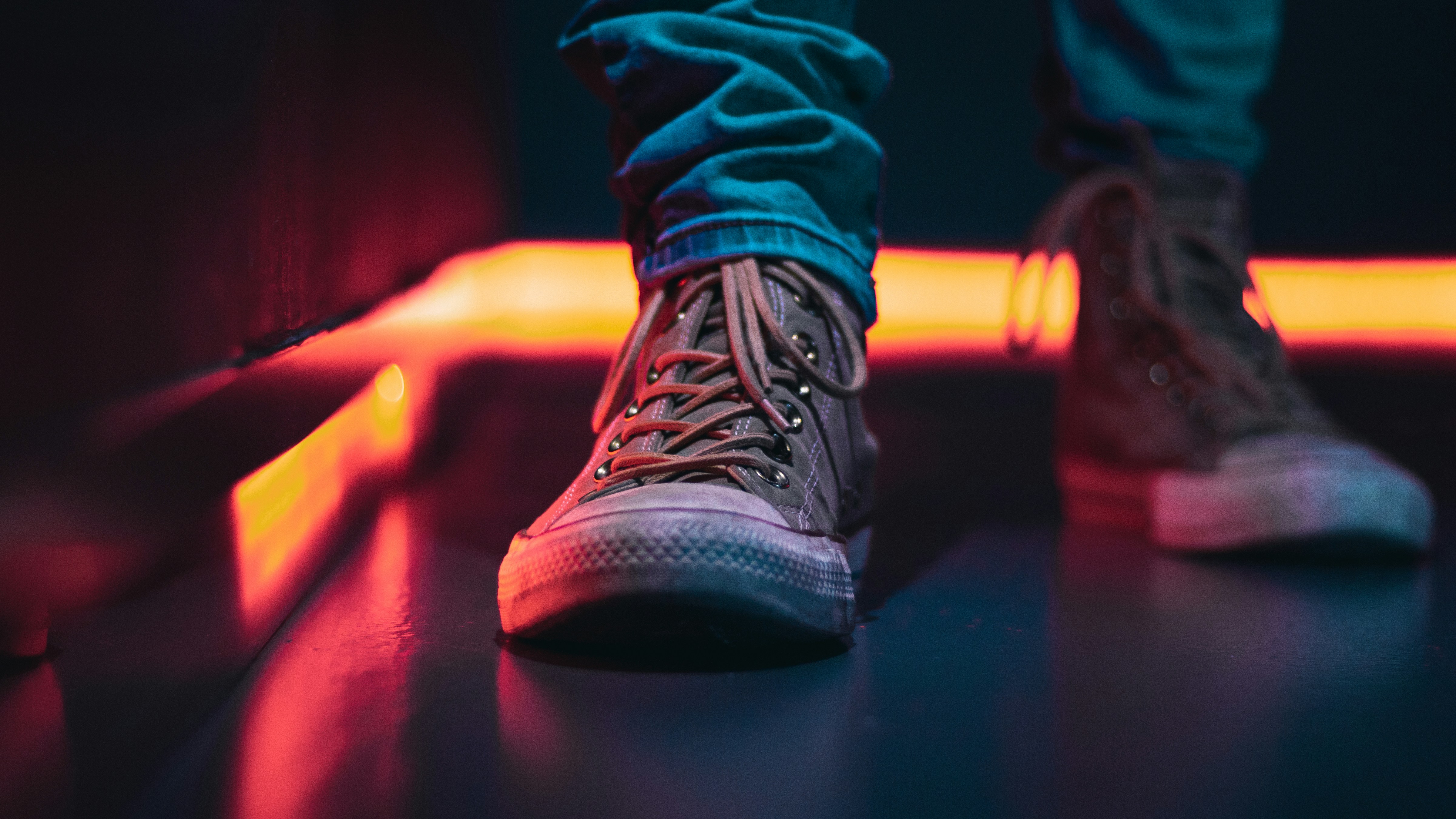 Close-up of a sneakered foot stepping on a reflective surface, illuminated by vibrant neon lighting.