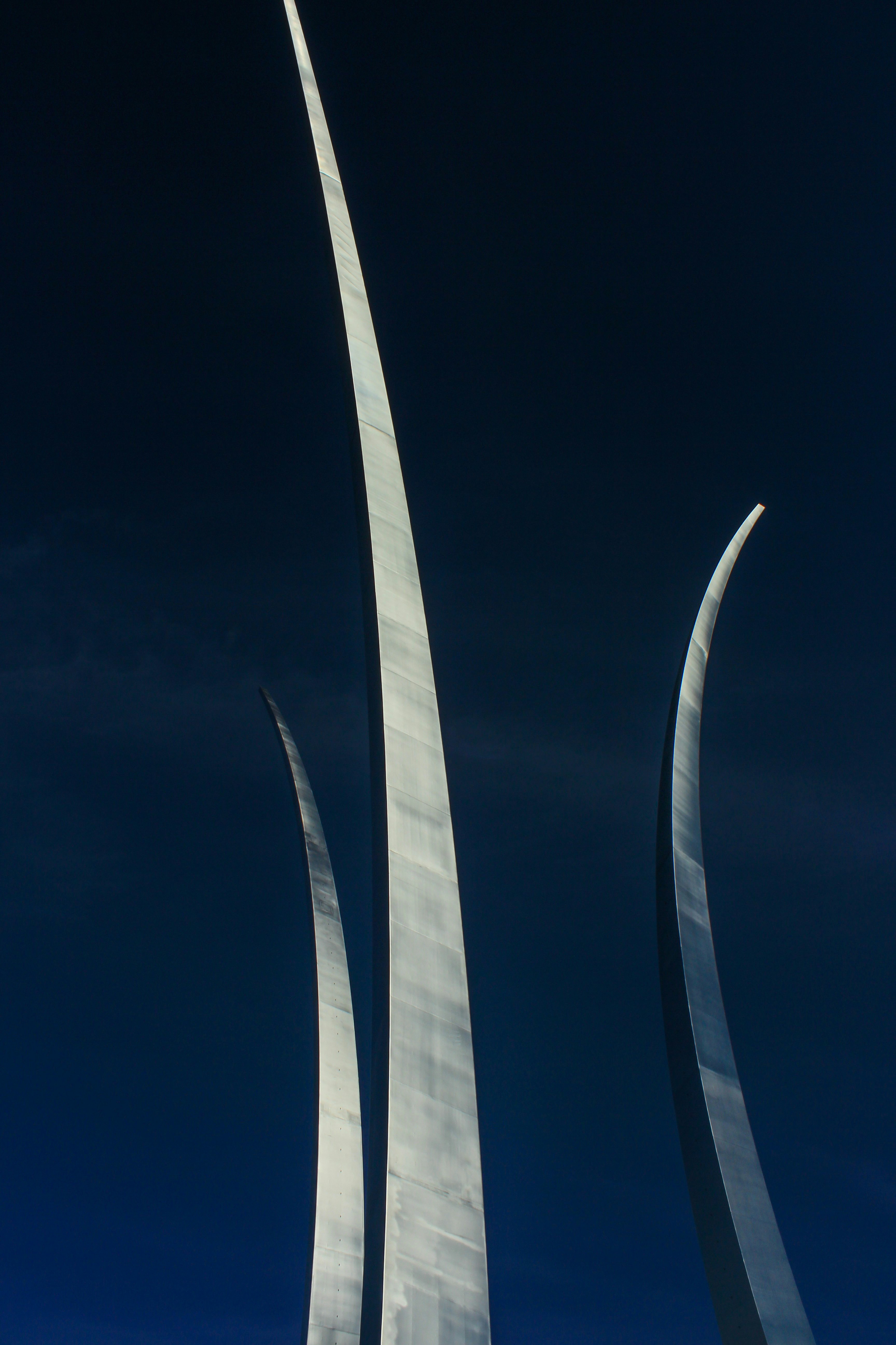 Sleek metallic sculptures rise dramatically against a deep blue sky, showcasing modern artistry and architectural elegance.