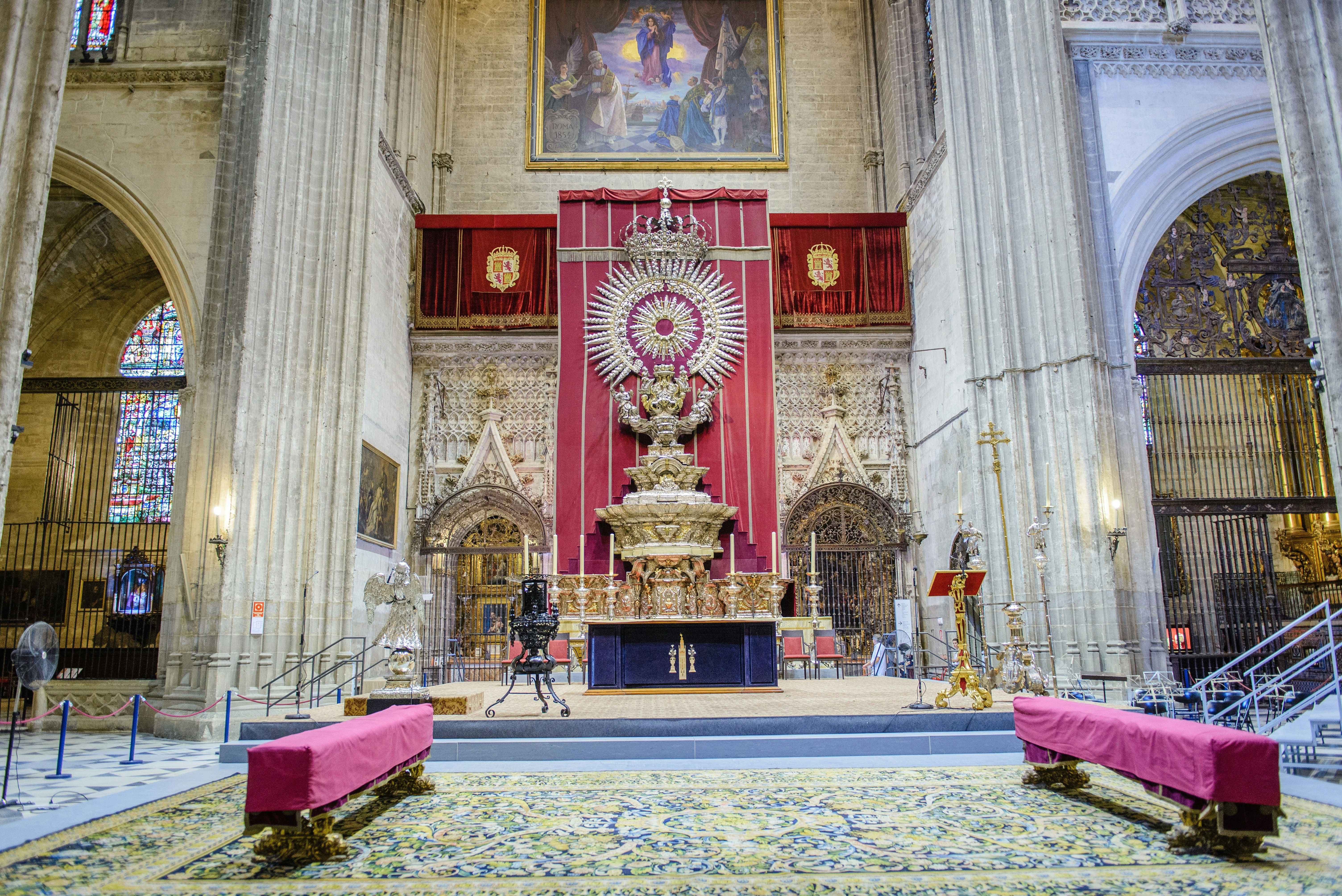 Ornate altar with red drapery and gold accents inside a grand cathedral.