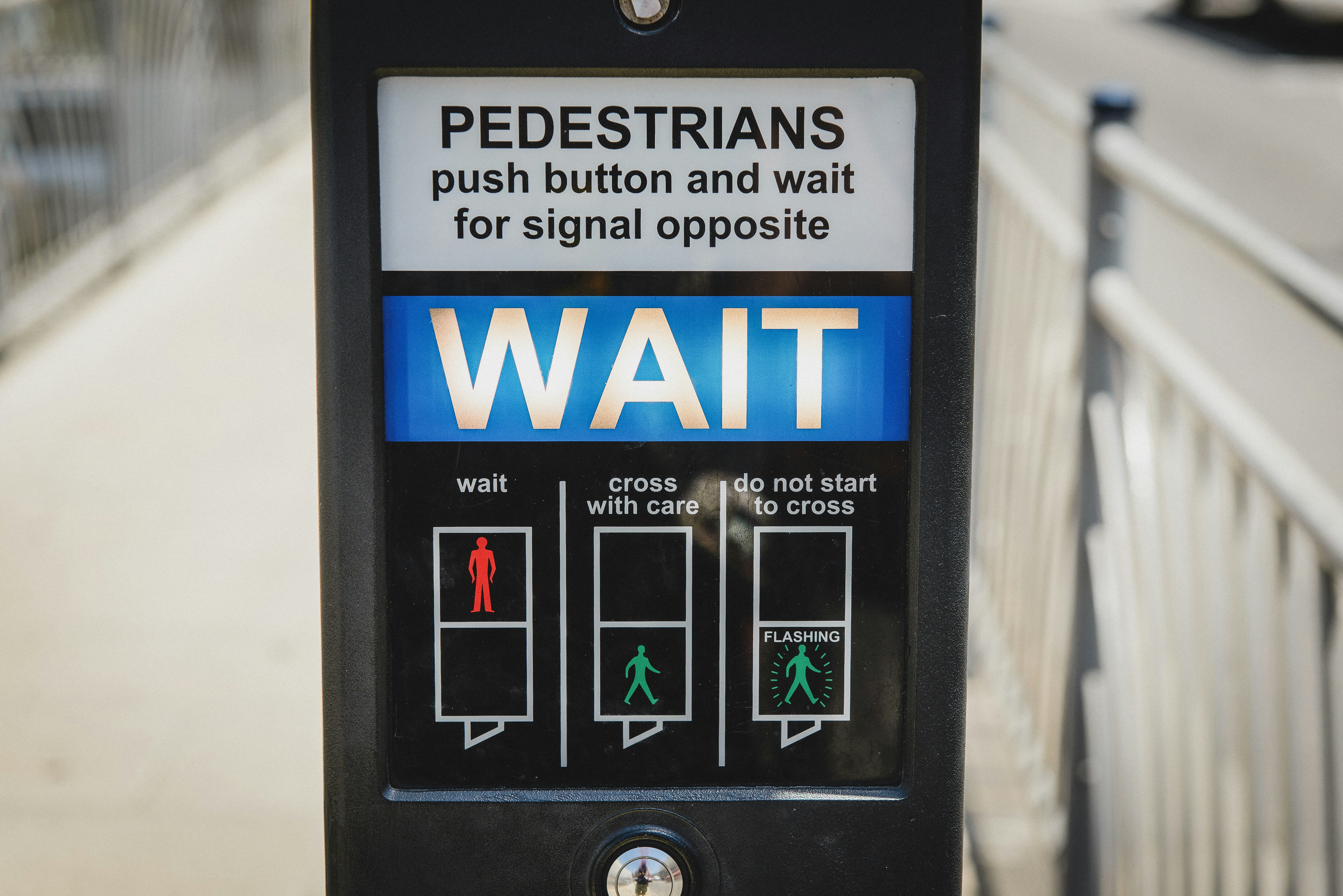 Sign instructing pedestrians to push the button and wait for the opposite signal, featuring clear visual cues for crossing.