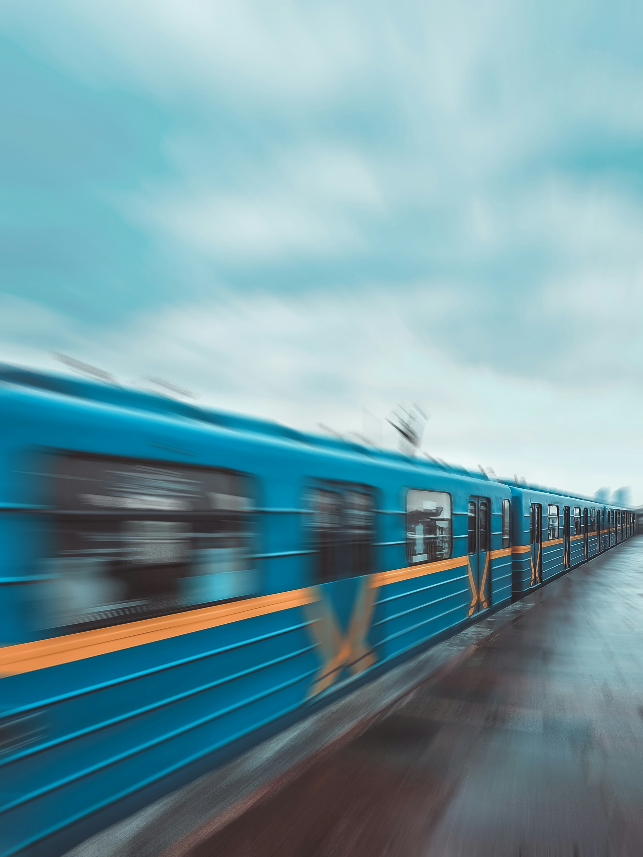 Blue commuter train streaks along a platform, with strong motion blur creating a vanishing perspective. This photograph emphasizes motion and depth.
