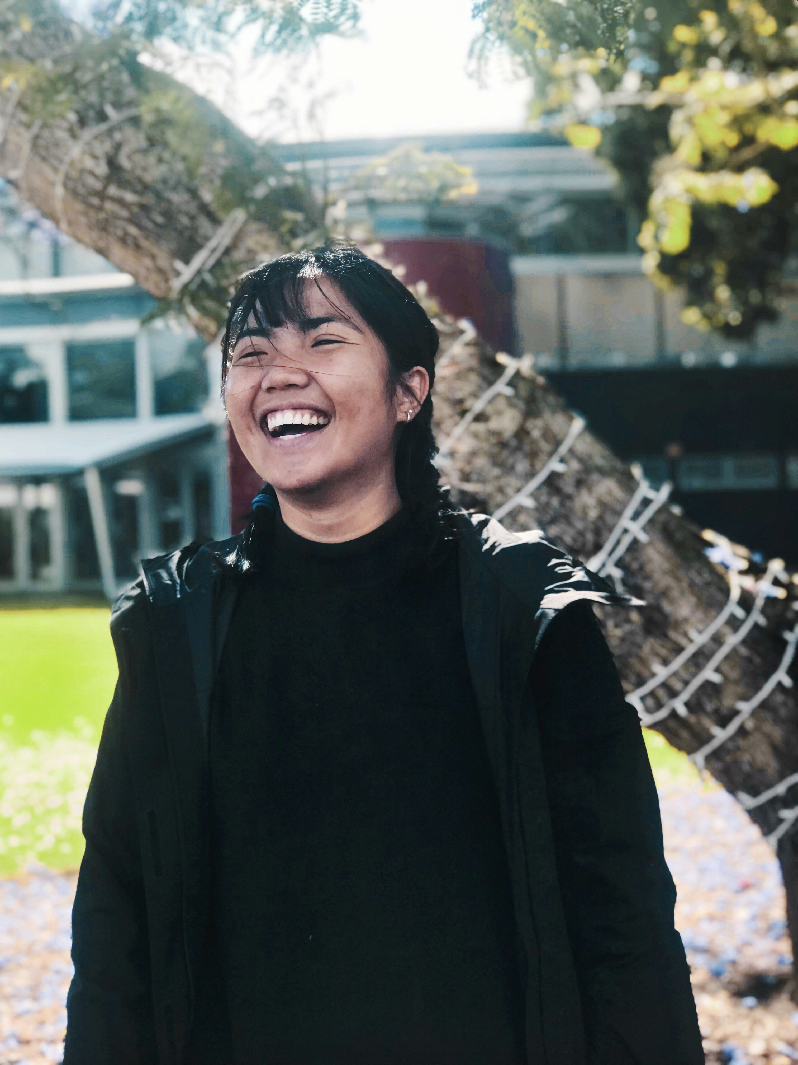 Joy in Sunlit Campus Shade: A candid smile beside a weathered tree
