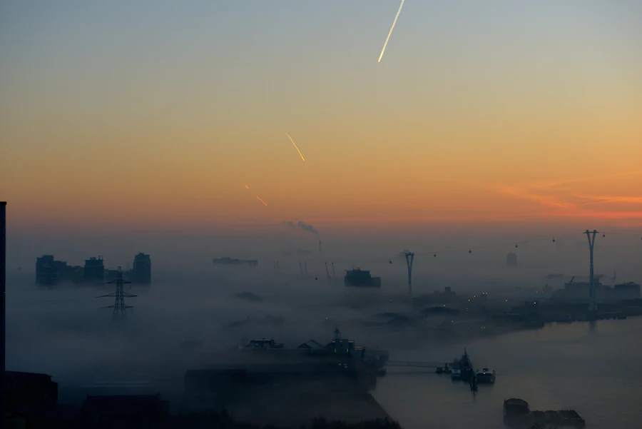 A serene harbor scene shrouded in morning fog, with faint silhouettes of buildings and vessels emerging as the sun rises. Contrails streak across the pastel sky.