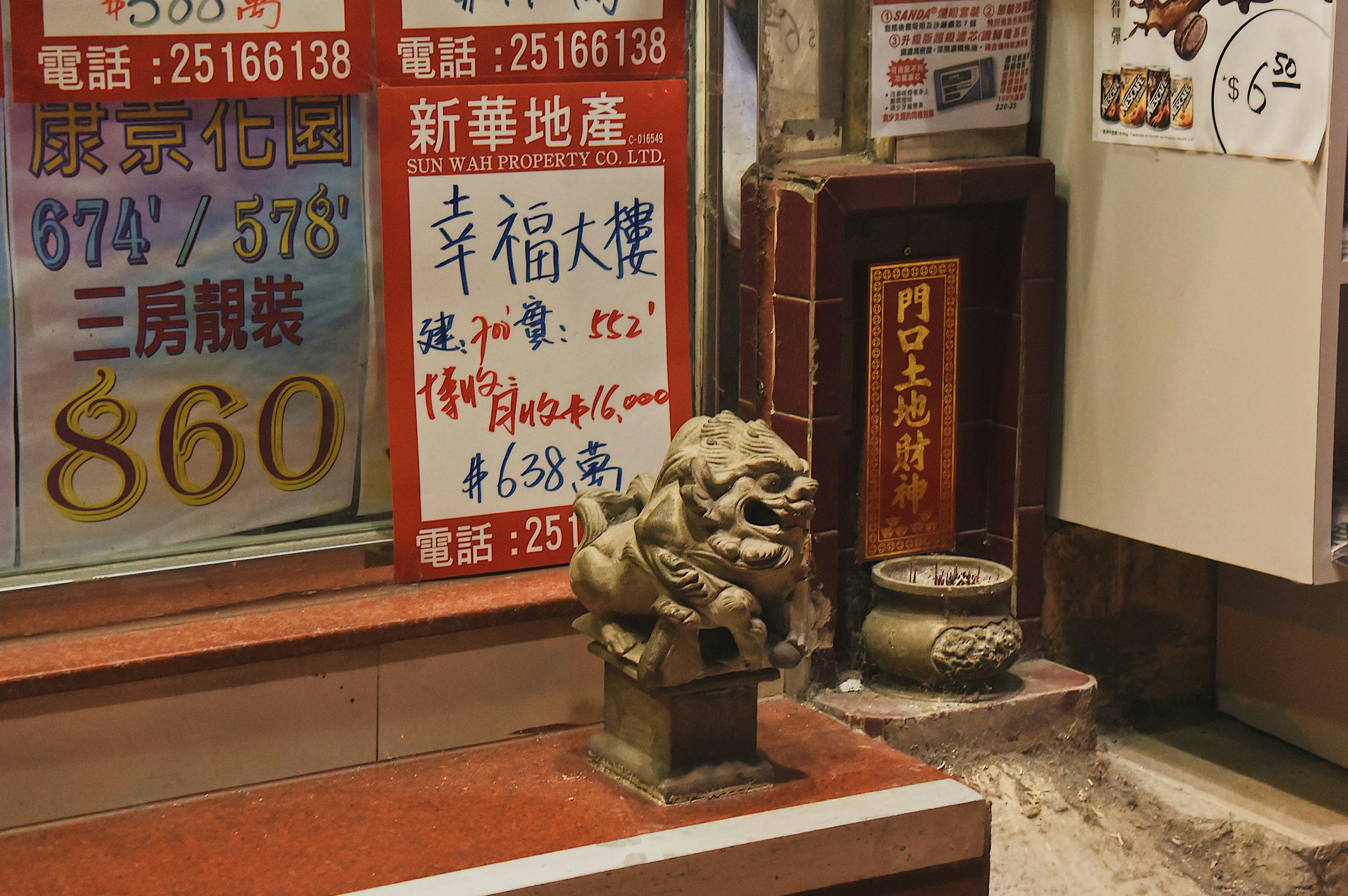 Stone lion statue beside a carved wooden pillar amid vibrant Chinese posters and signage.