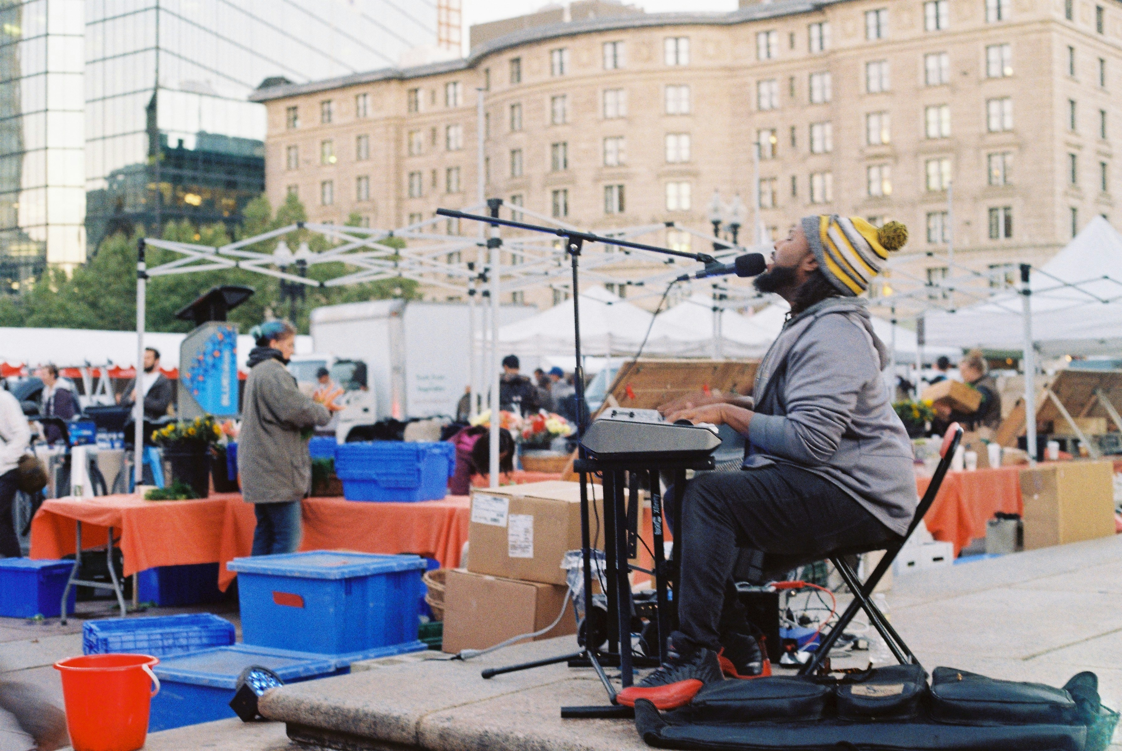 Man playing keyboard and singing on stage near people and building ...