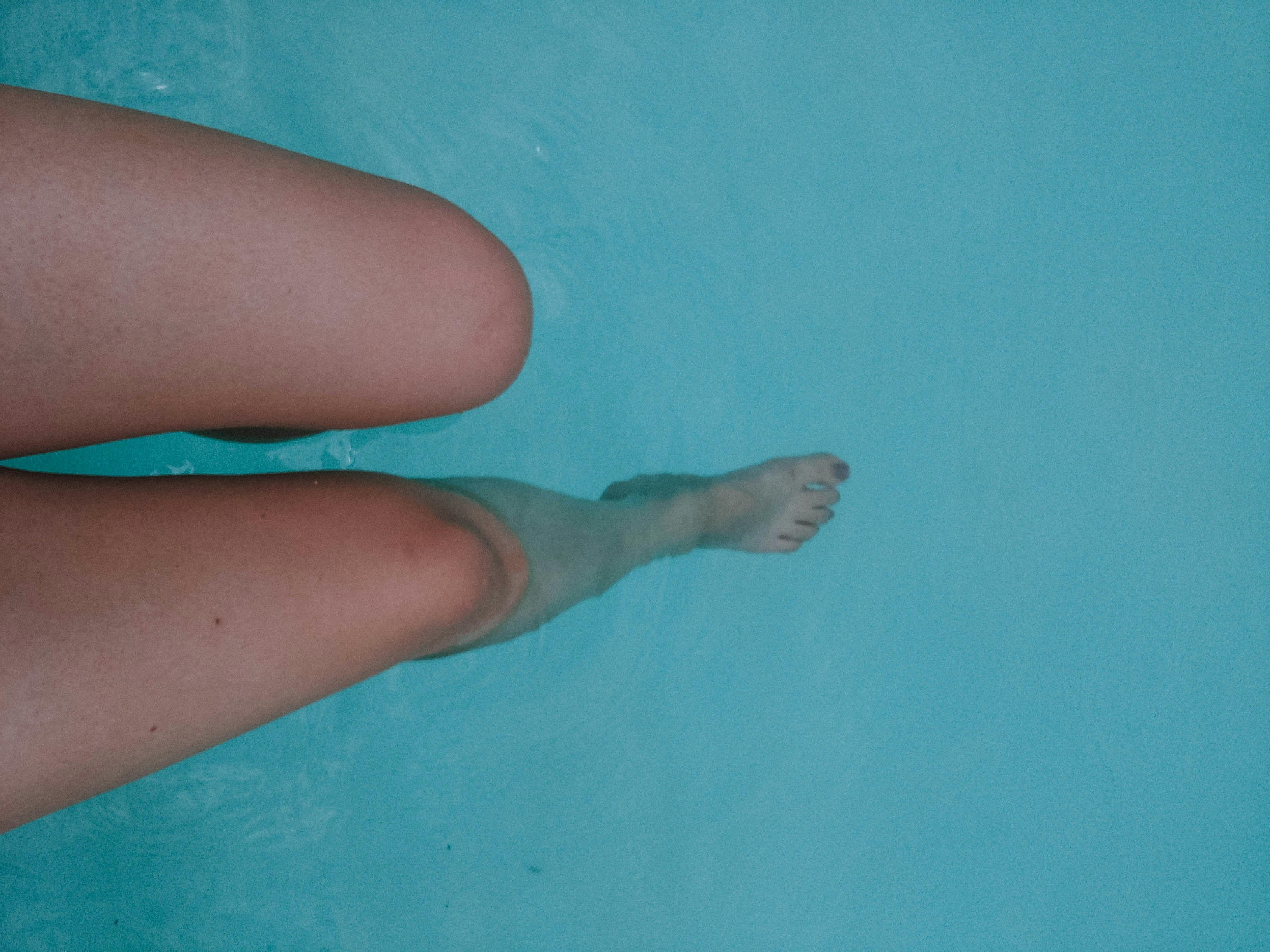 A pair of legs submerged in tranquil blue water, highlighting the contrast between skin tone and the pool's surface. The image evokes a sense of relaxation and leisure.