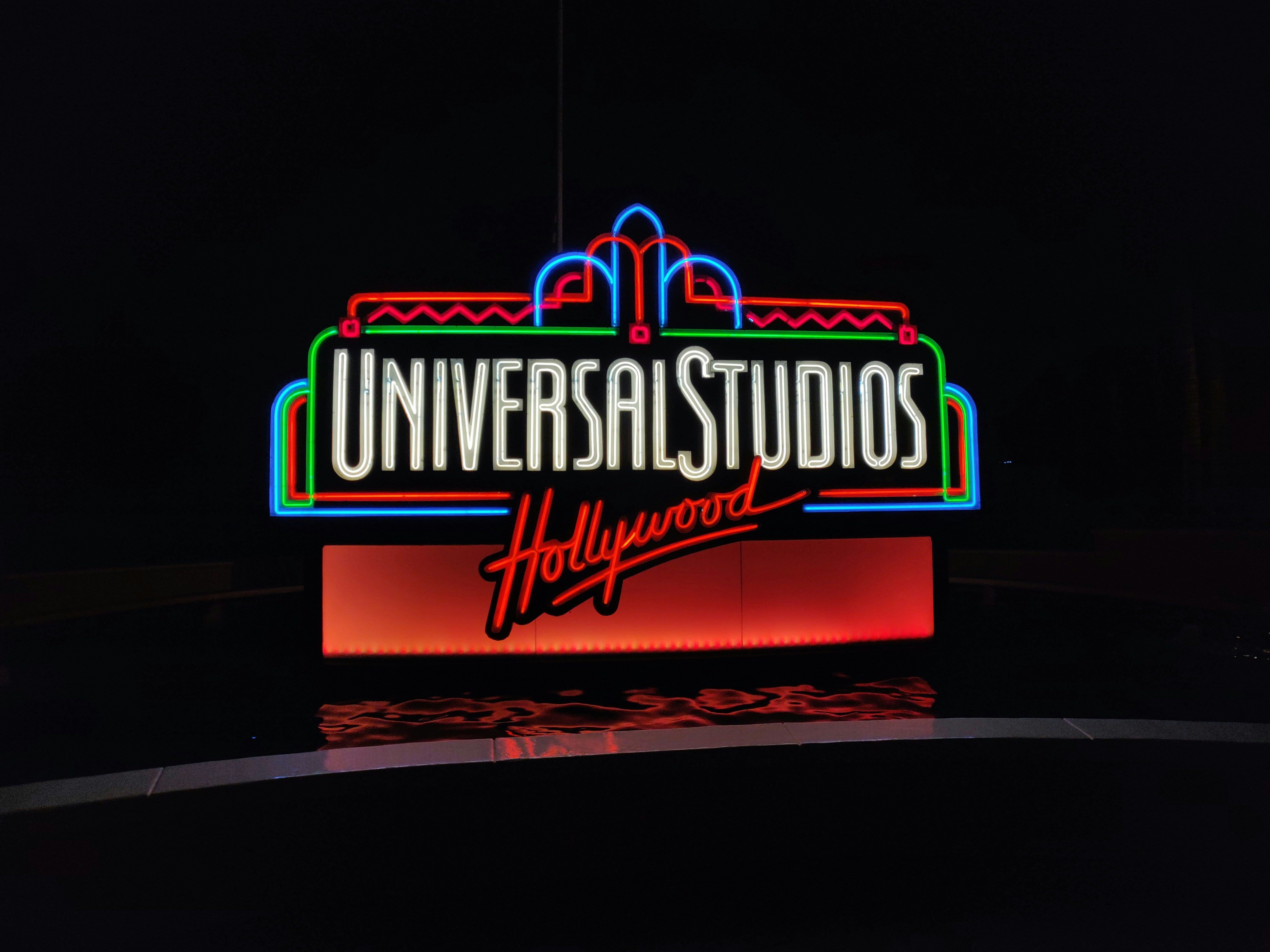 Illuminated Universal Studios Hollywood neon sign glowing against a dark background.