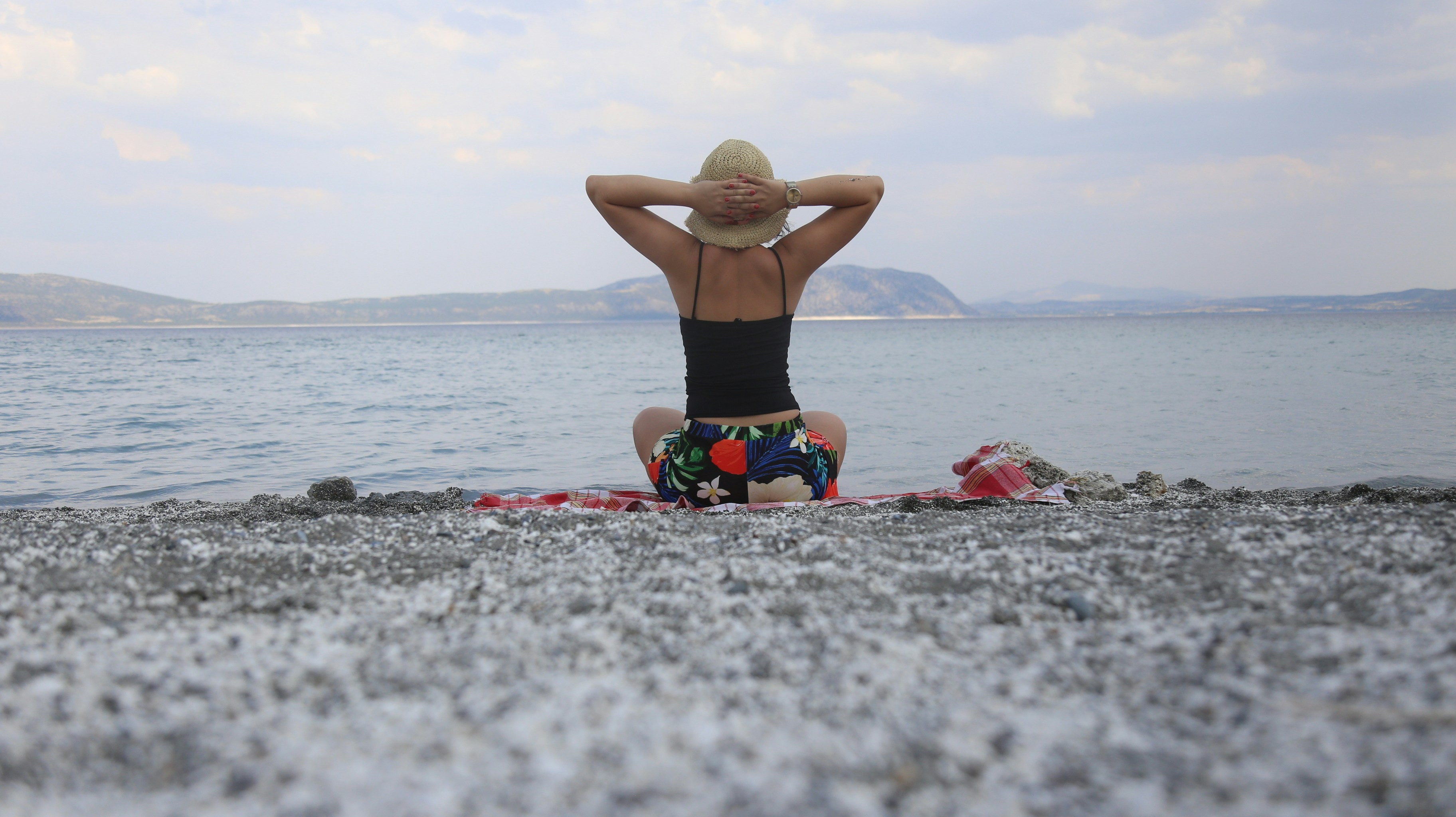 Woman relaxing on a beach towel, gazing at the calm sea under a cloudy sky.