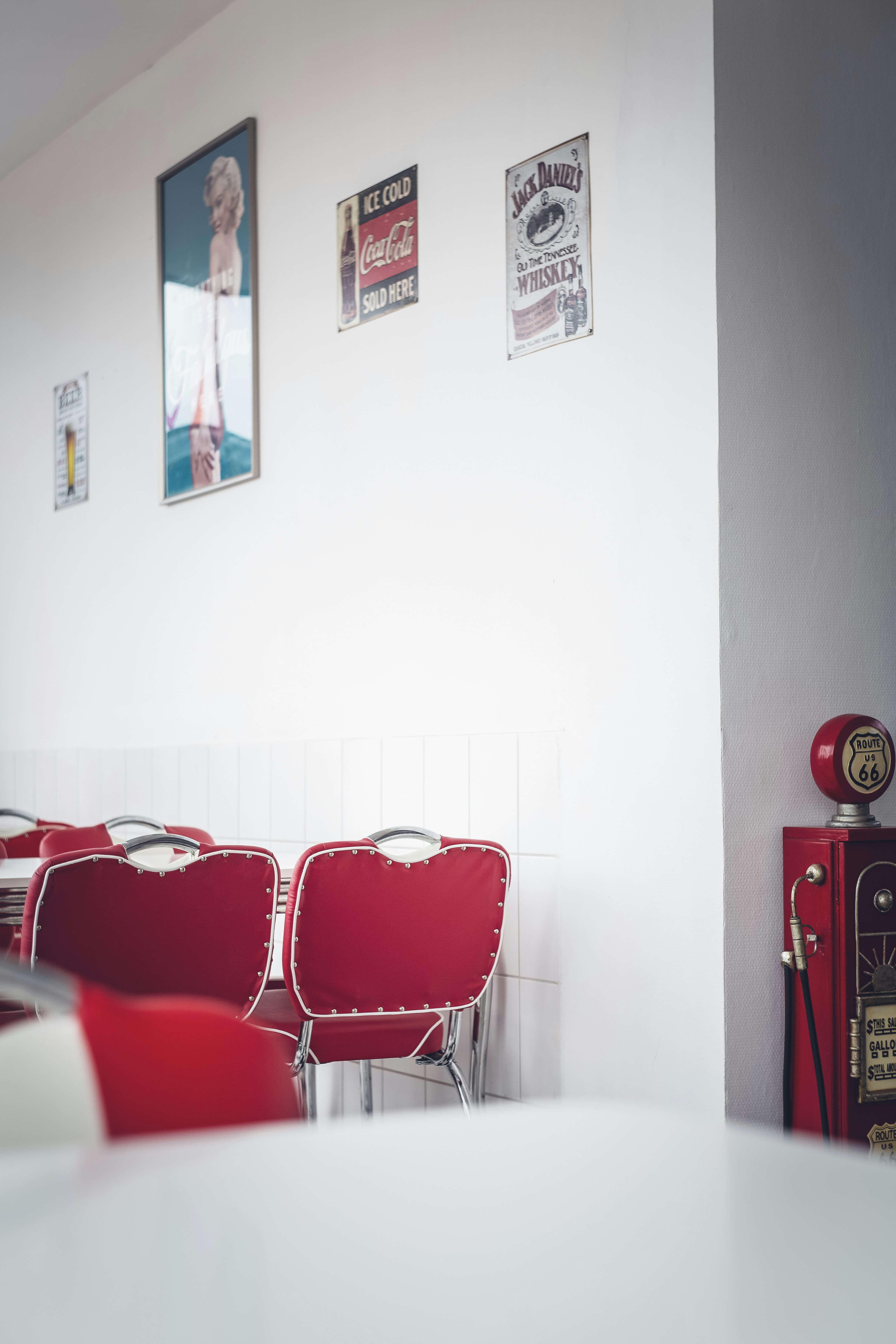Charming red diner chairs set against a minimalist white wall adorned with vintage advertisements. A classic gas pump adds to the nostalgic atmosphere.