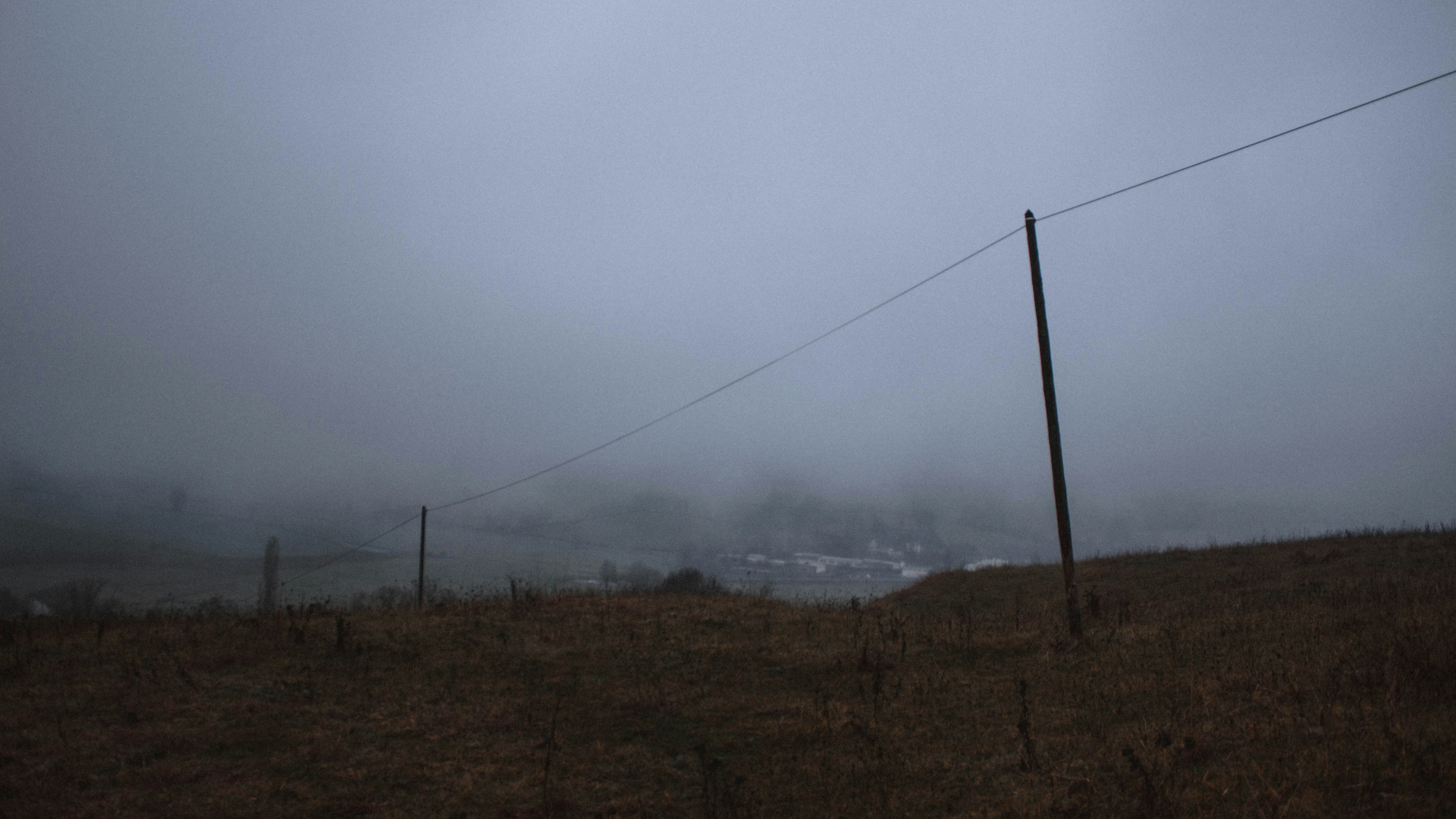 Fog envelops a rural landscape, with a lone telephone pole standing against the muted backdrop of distant hills. The scene evokes a sense of solitude and tranquility.